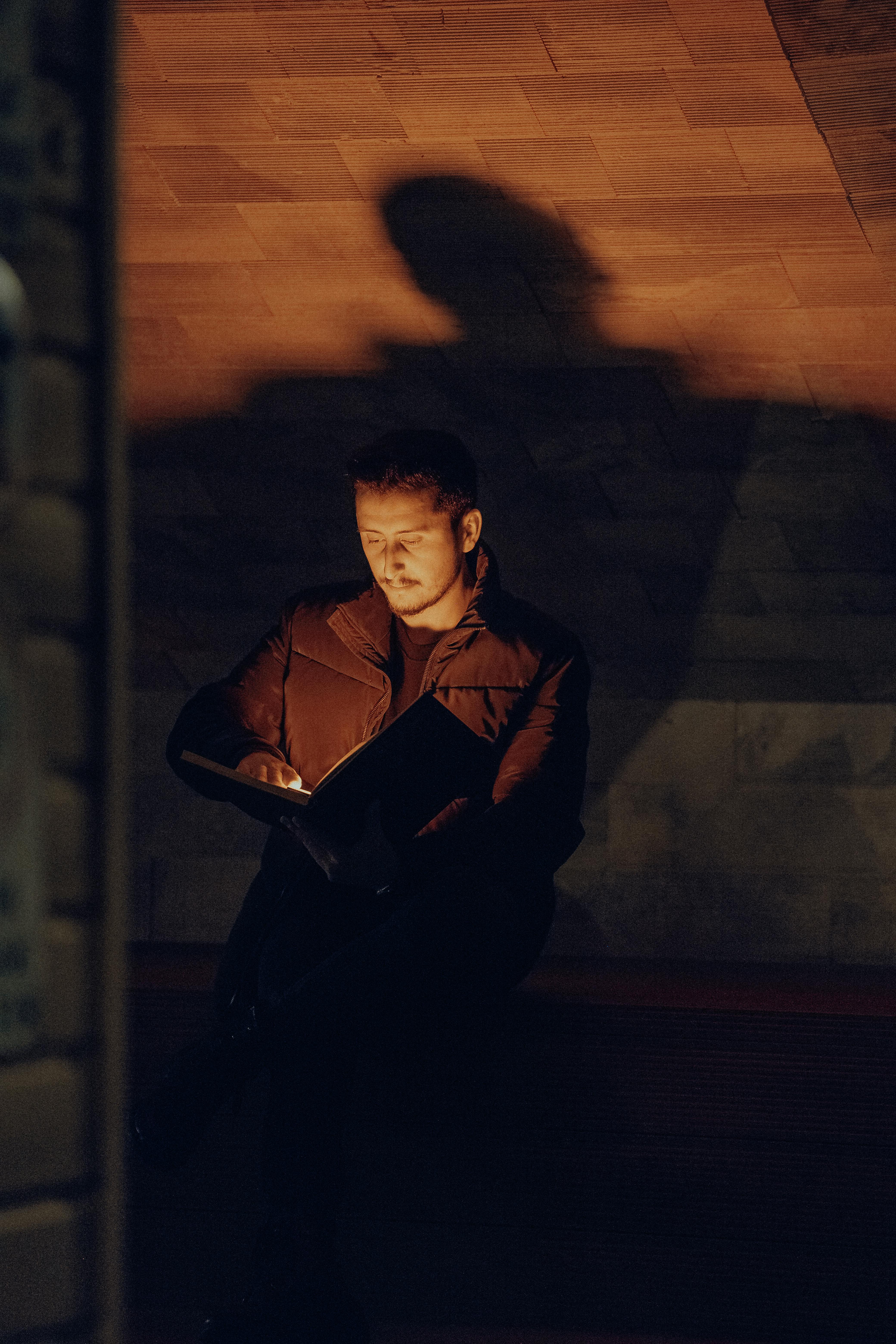 Man Sitting in Darkness and Reading Book · Free Stock Photo