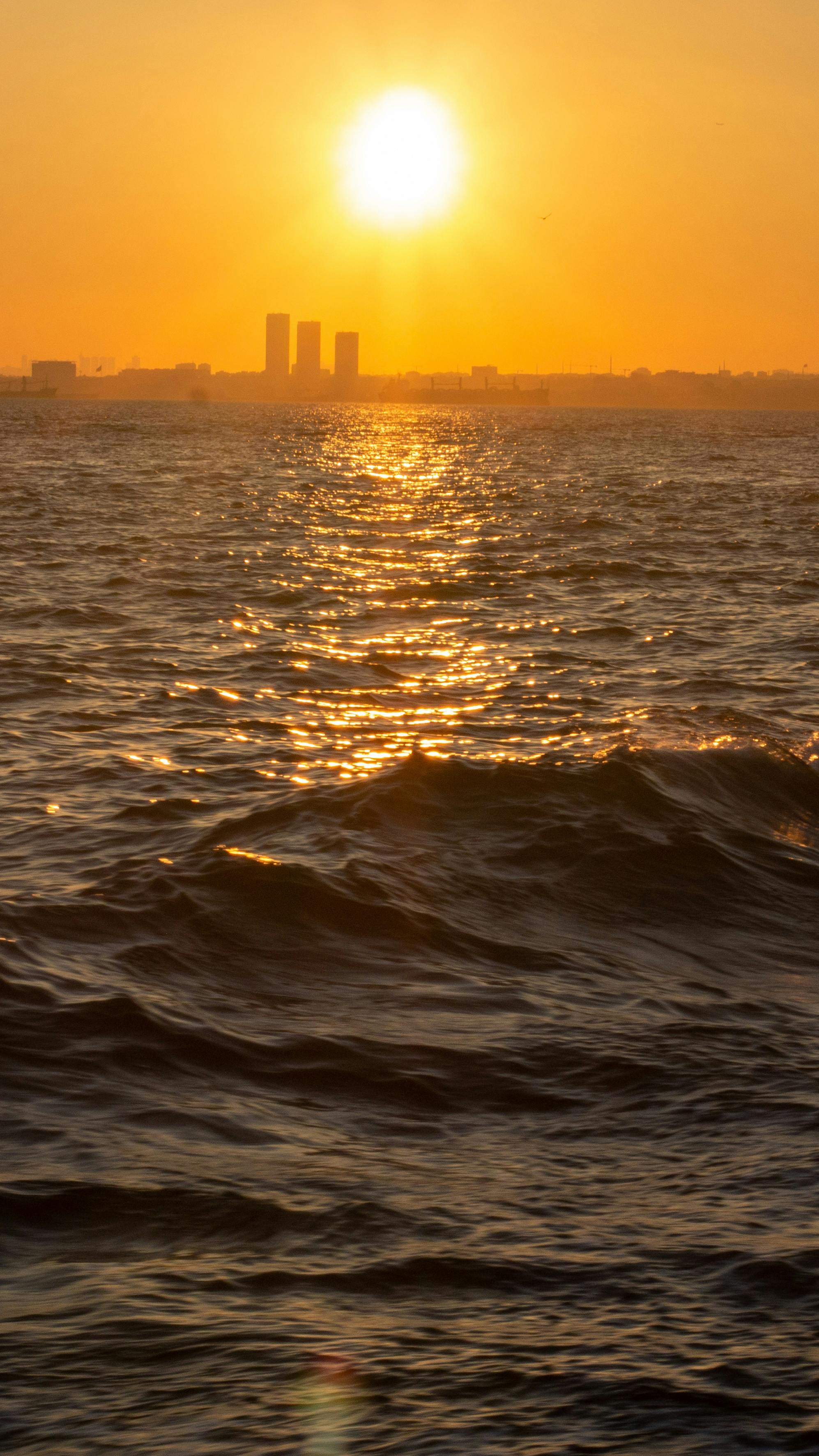 Sun on Clear, Yellow Sky over Sea Shore with City behind at Sunset ...
