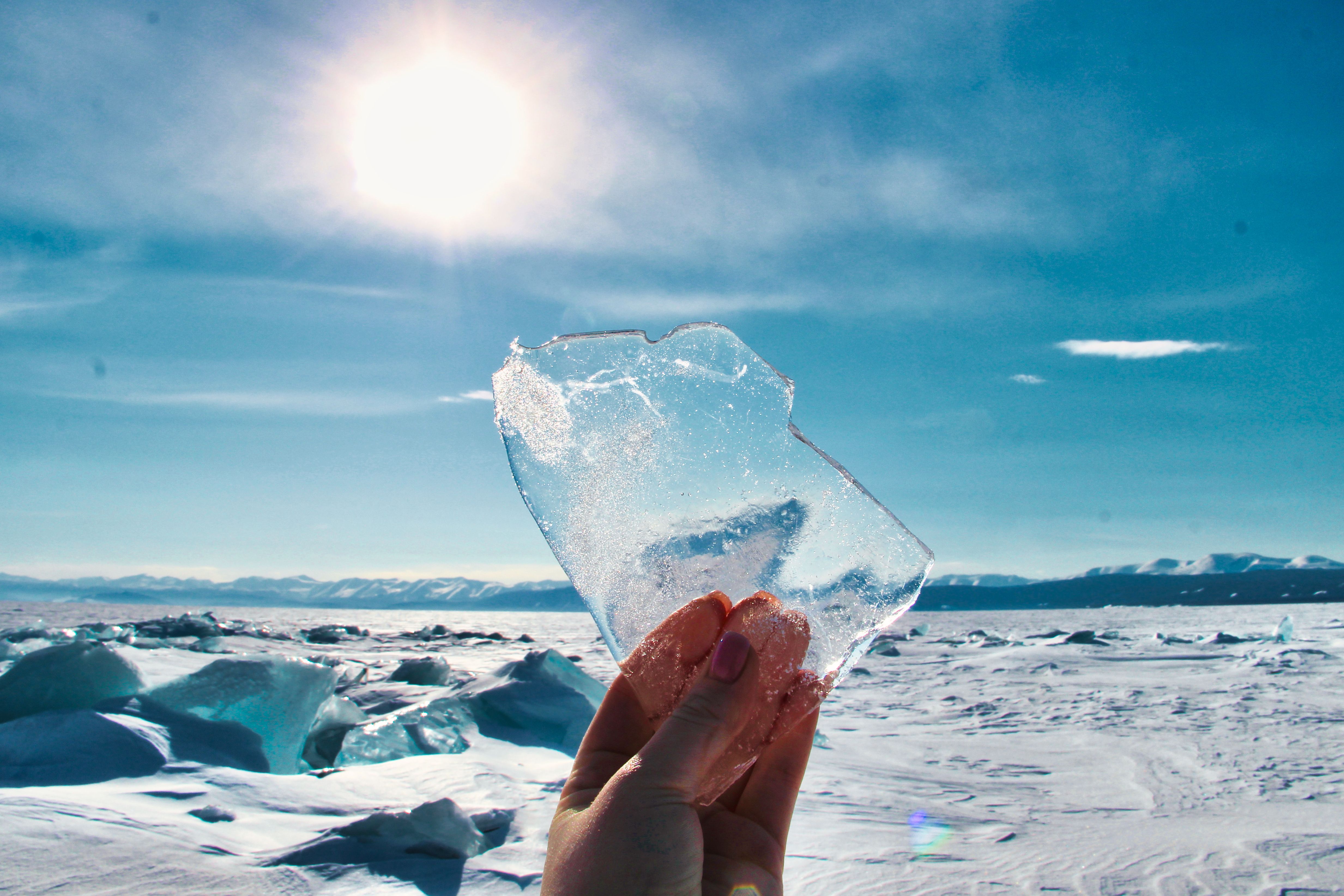 A person holding up a piece of ice in front of the sun · Free Stock Photo
