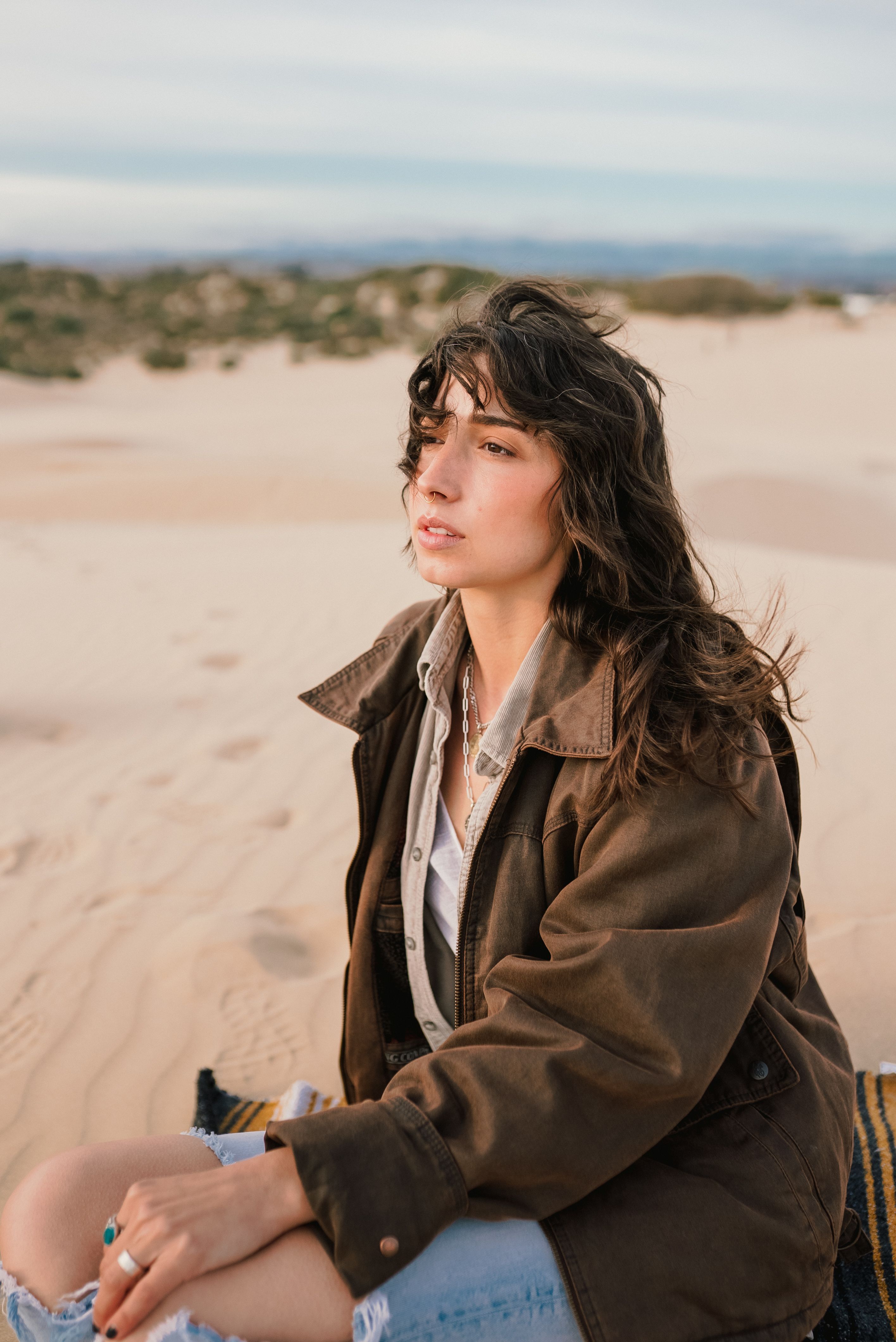 Brunette Woman in Jacket Sitting on Sand · Free Stock Photo