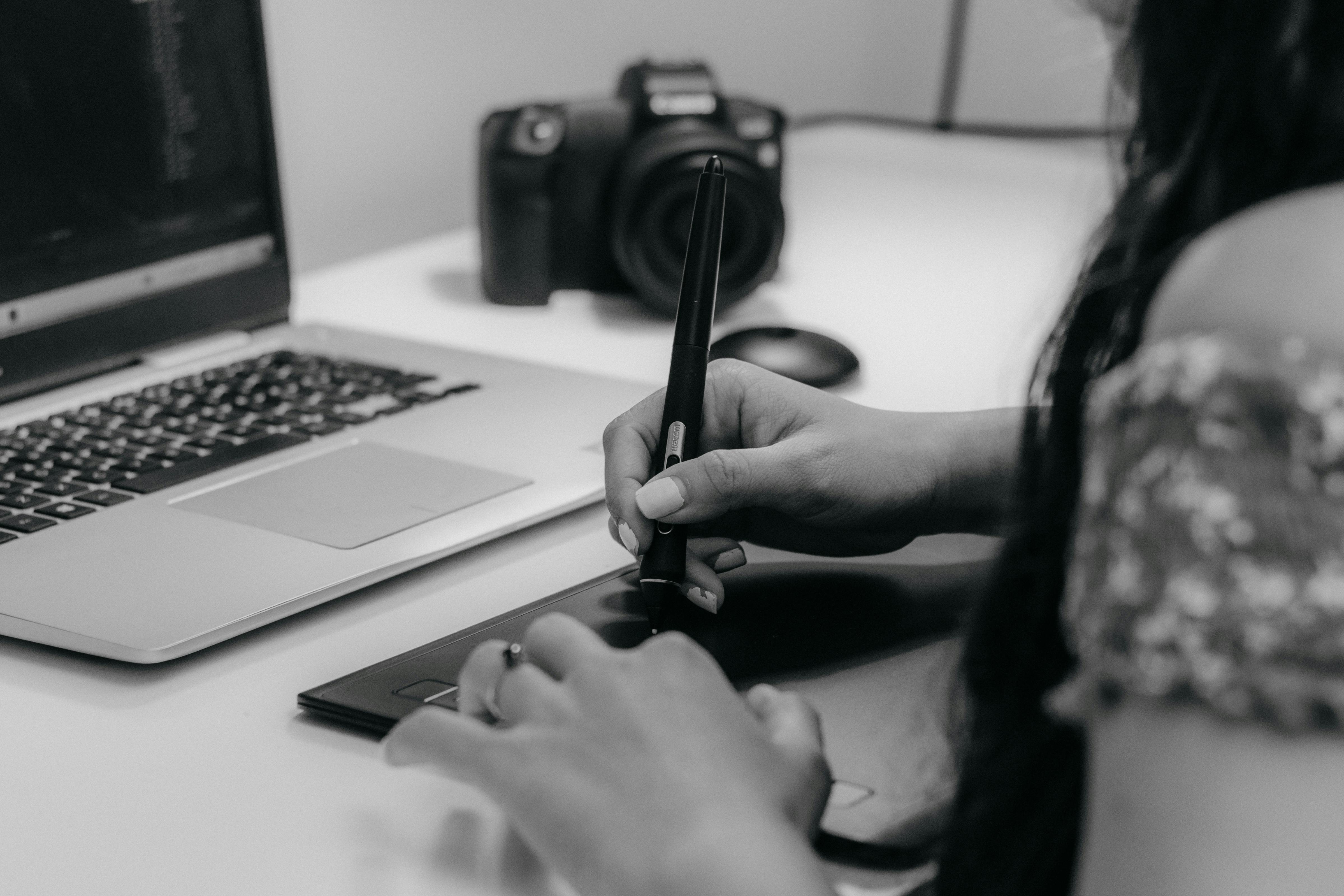 A woman is using a pen to draw on a laptop · Free Stock Photo