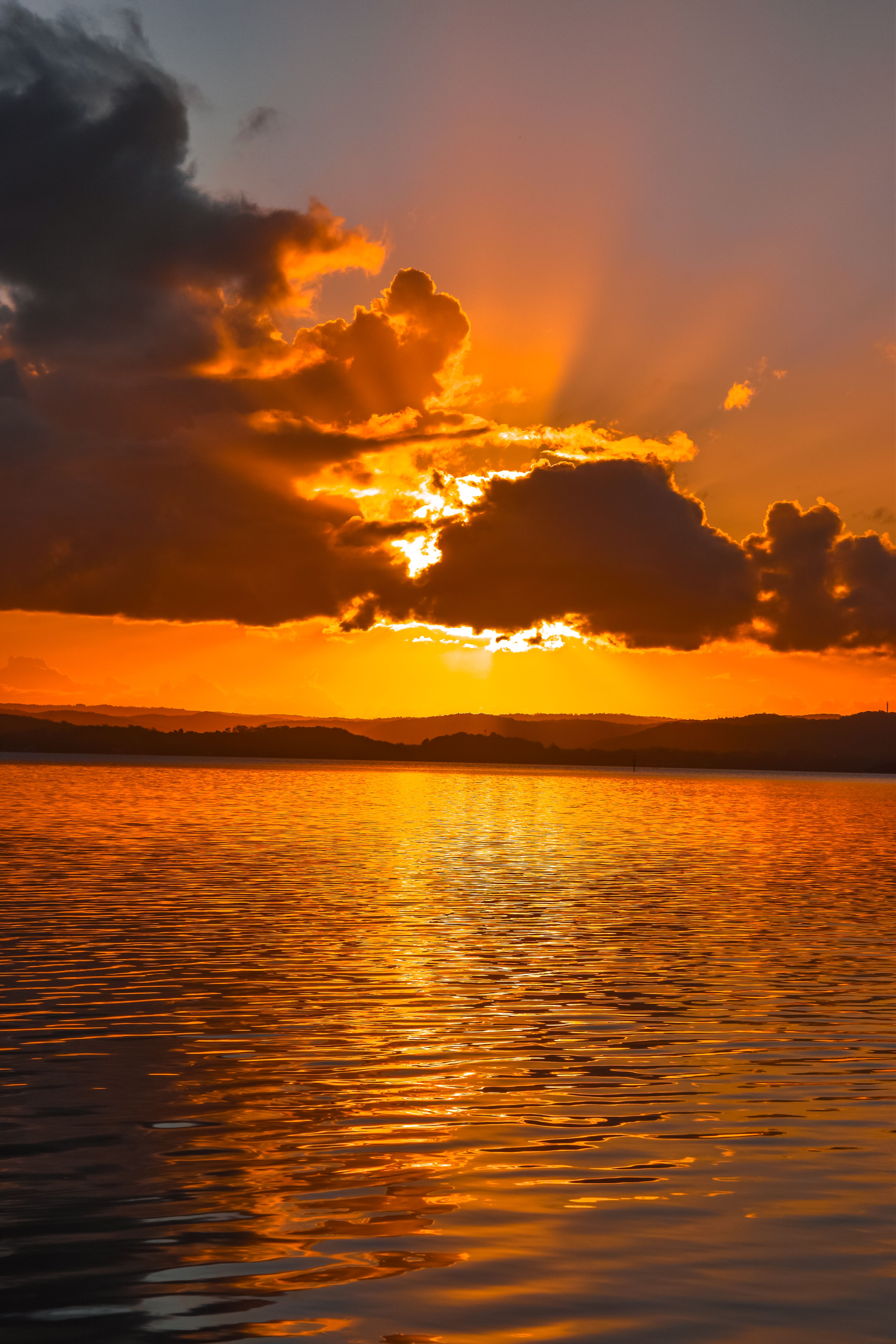 A sunset over the water with clouds in the sky · Free Stock Photo
