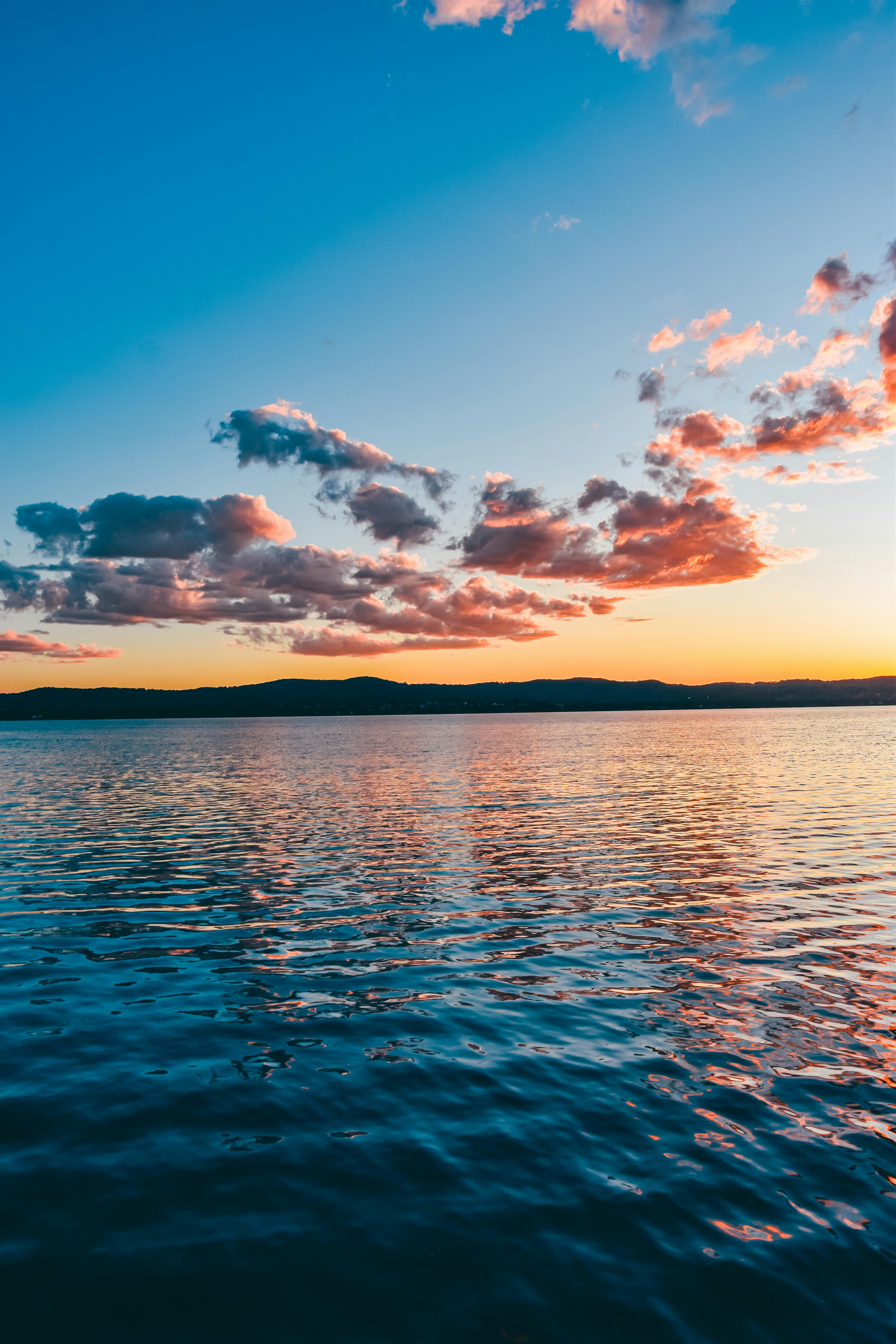 A sunset over the water with clouds and water · Free Stock Photo