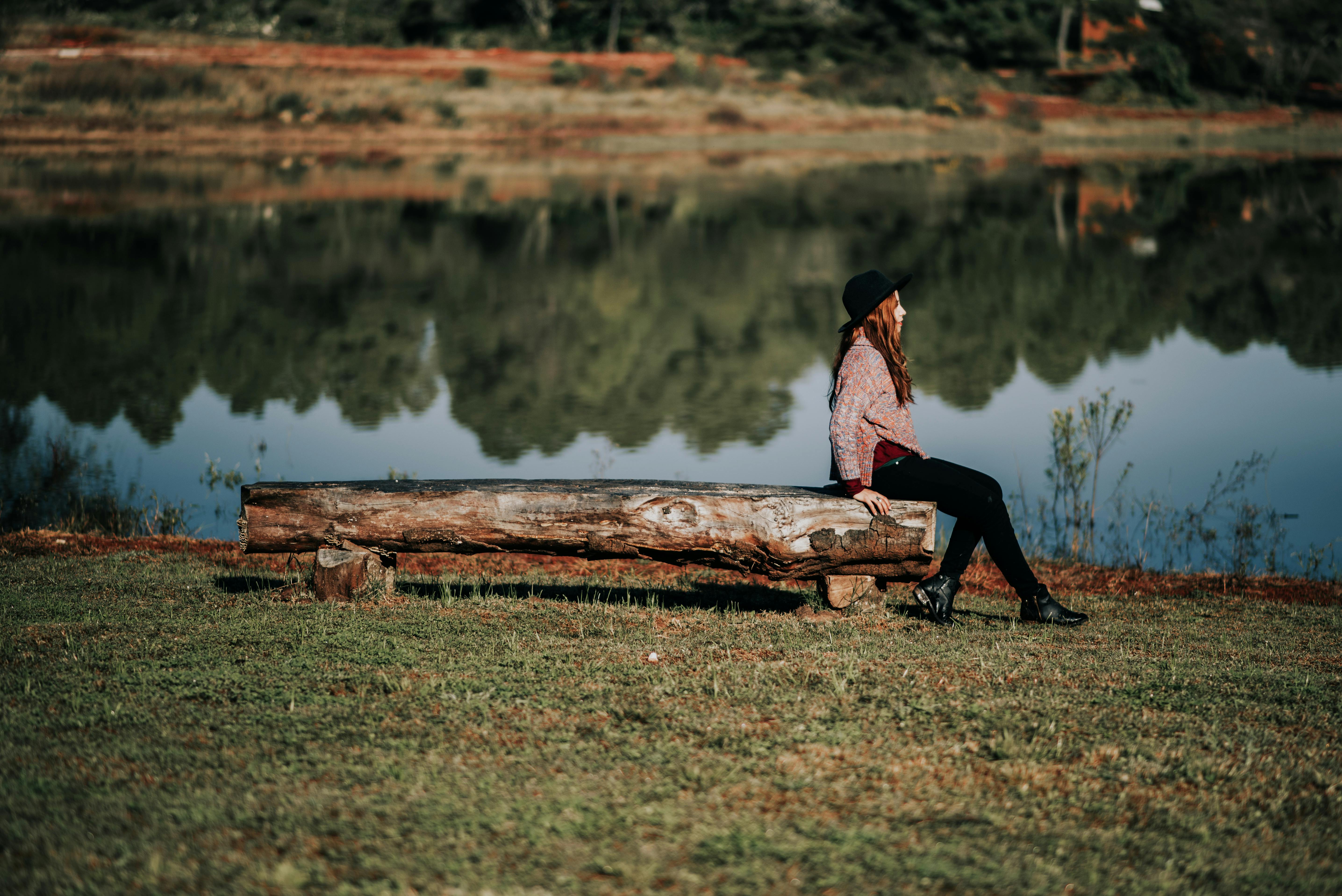 Woman Sitting on Log Near Body of Water · Free Stock Photo