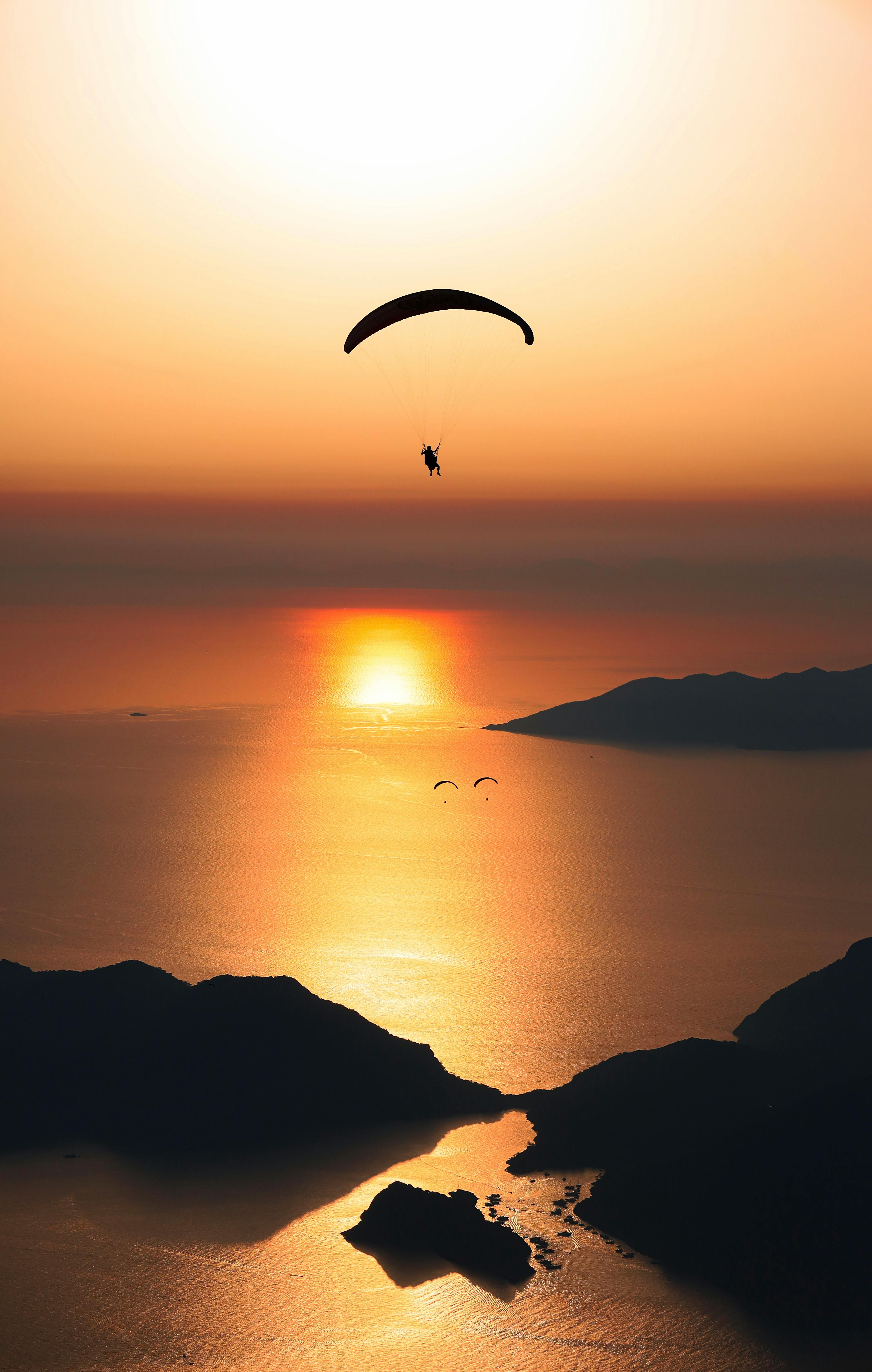 Aerial View of Silhouetted Shore and a Person Flying with a Parachute ...