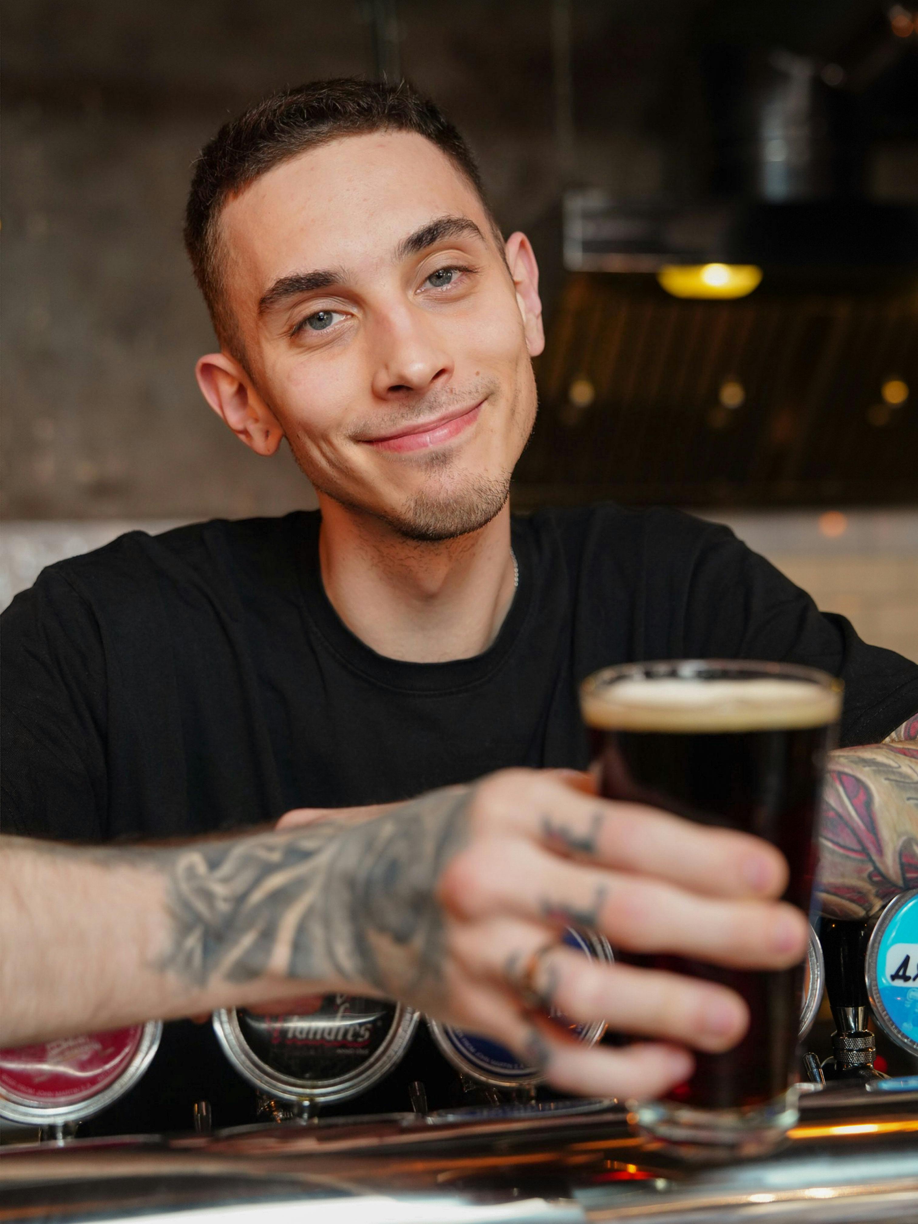 Smiling Bartender Serving a Glass of Guinness · Free Stock Photo
