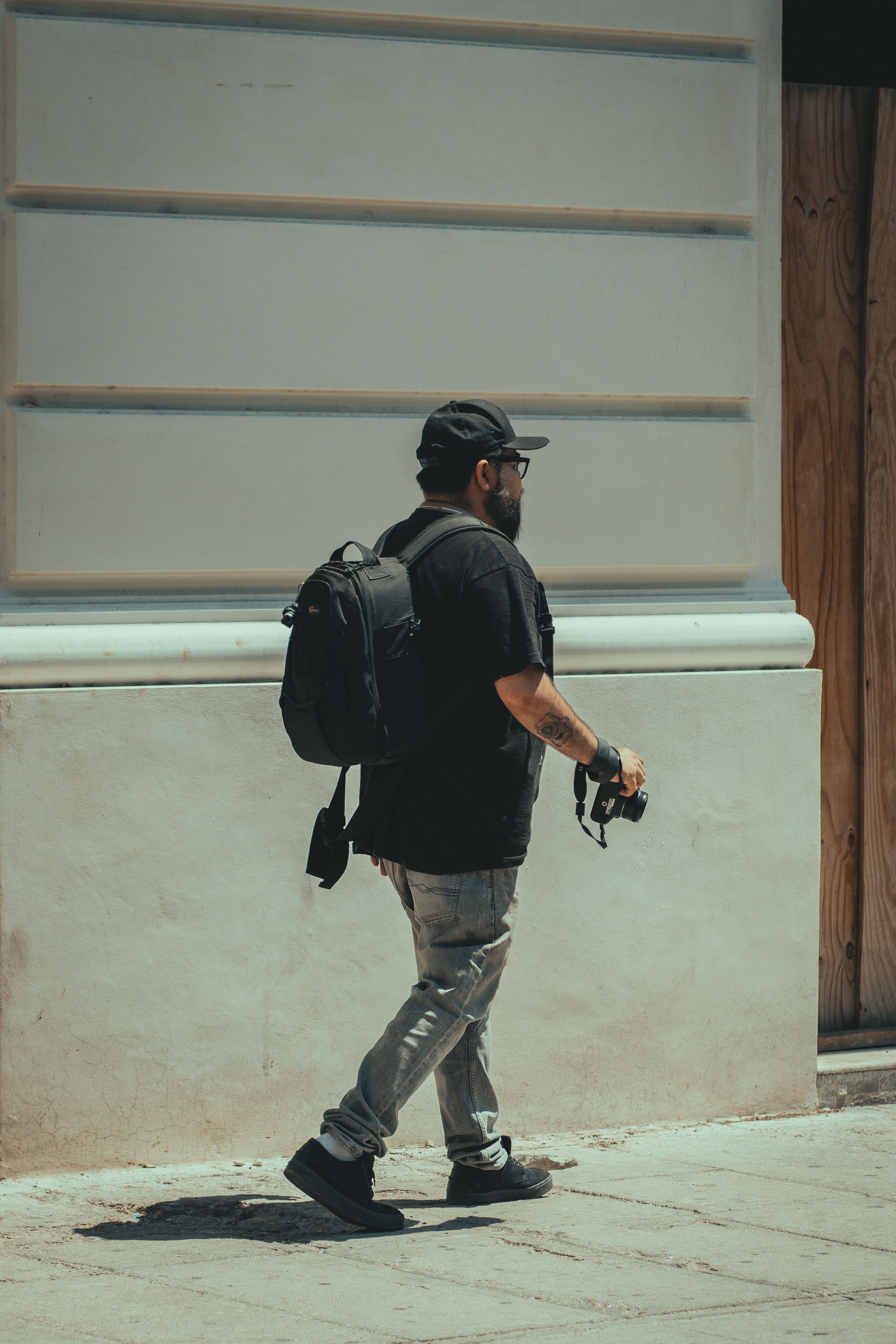 A Photographer Holding a Camera Walking on the Sidewalk · Free Stock Photo