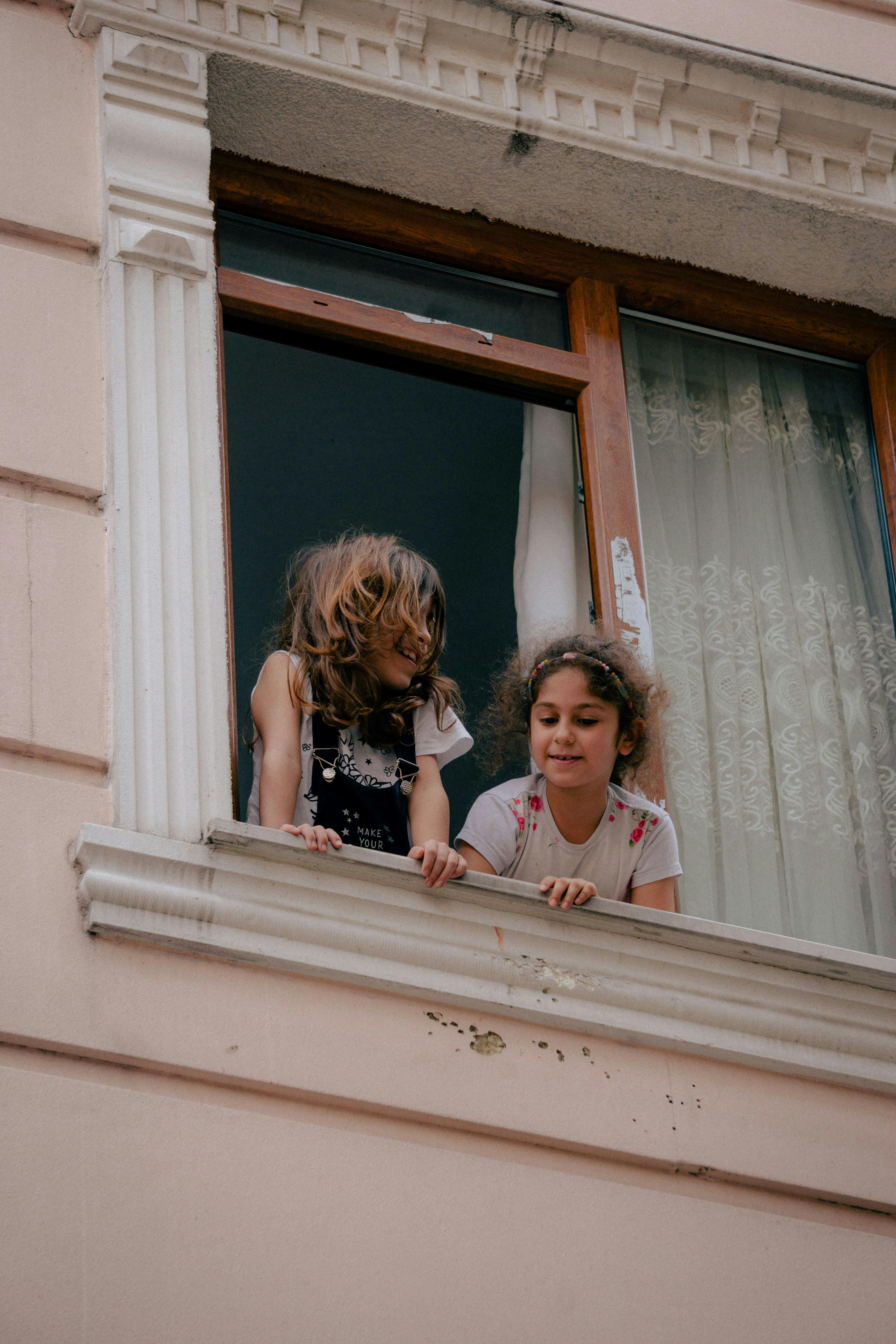 Two young girls looking out of a window · Free Stock Photo