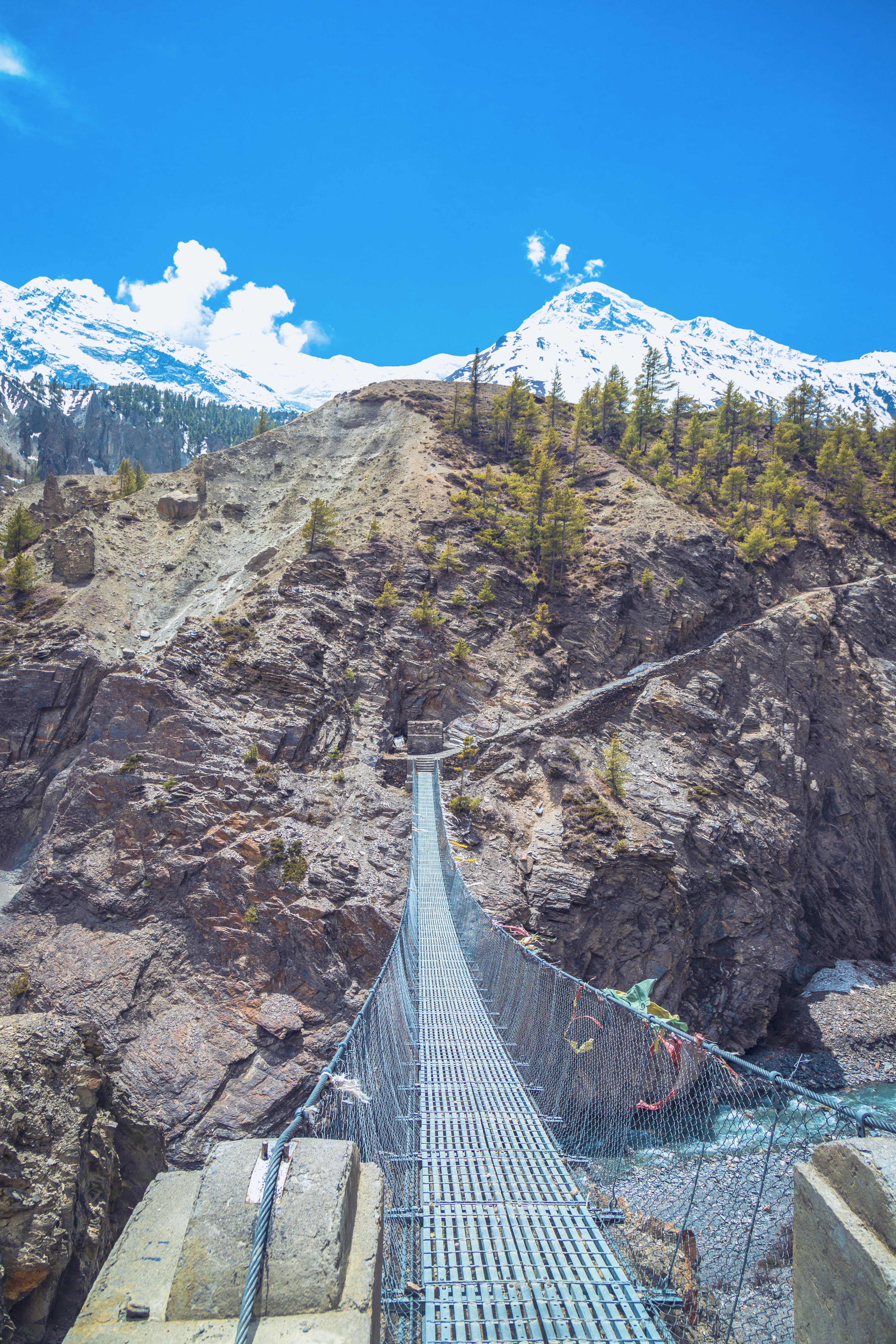 A suspension bridge over a river with mountains in the background ...