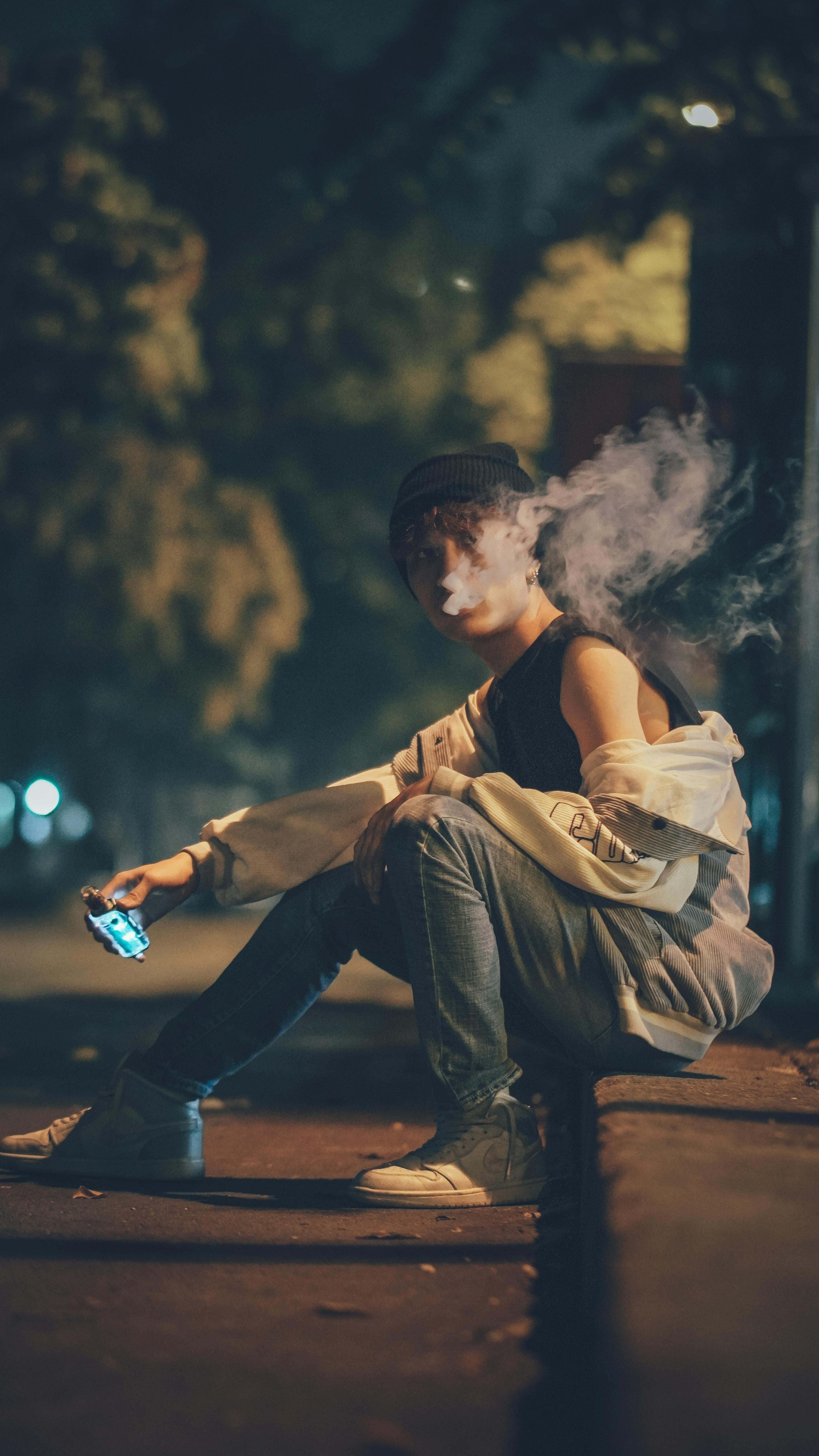 Young Man Sitting on Street Curb and Vaping · Free Stock Photo