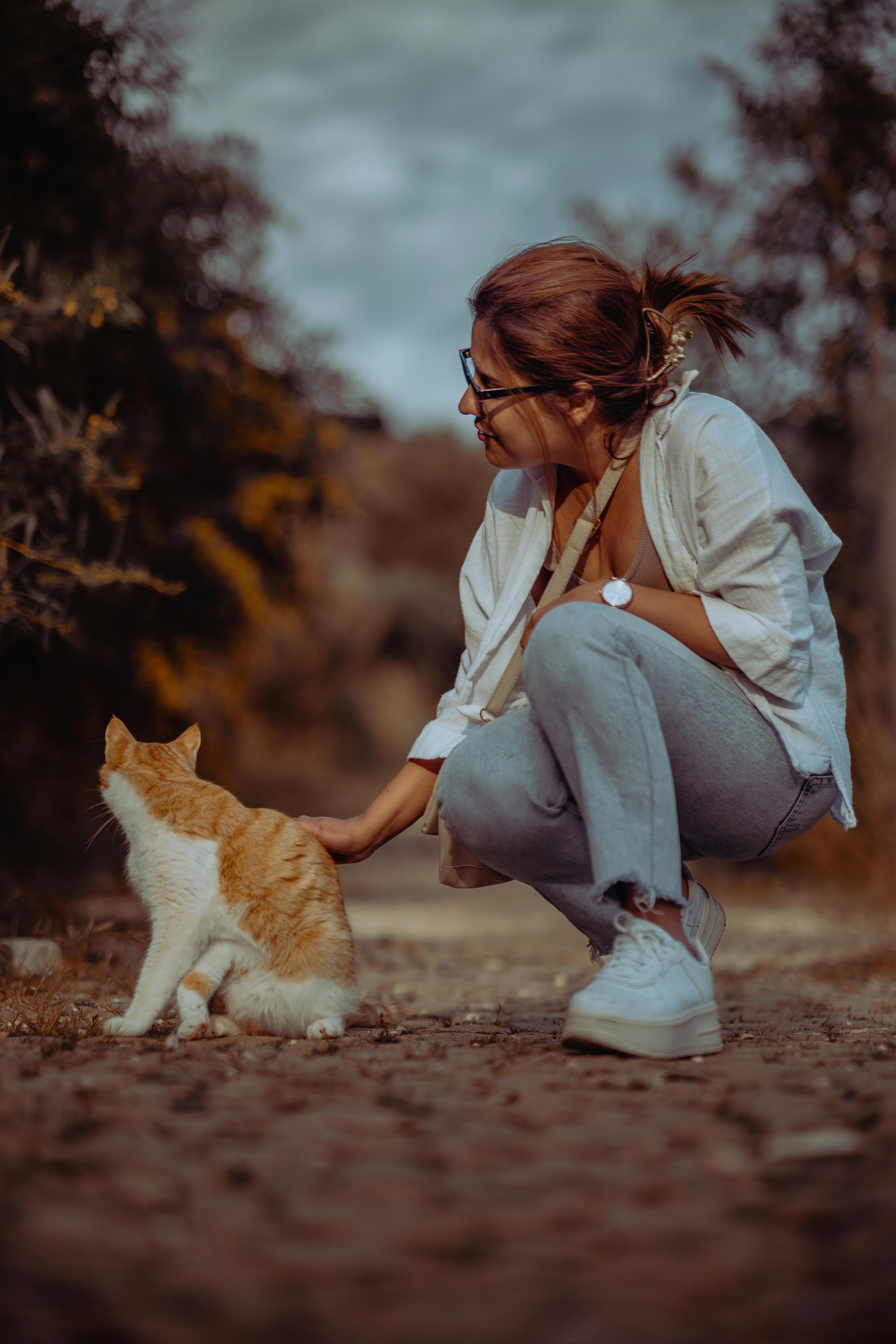 Woman Patting Cat on Pavement · Free Stock Photo