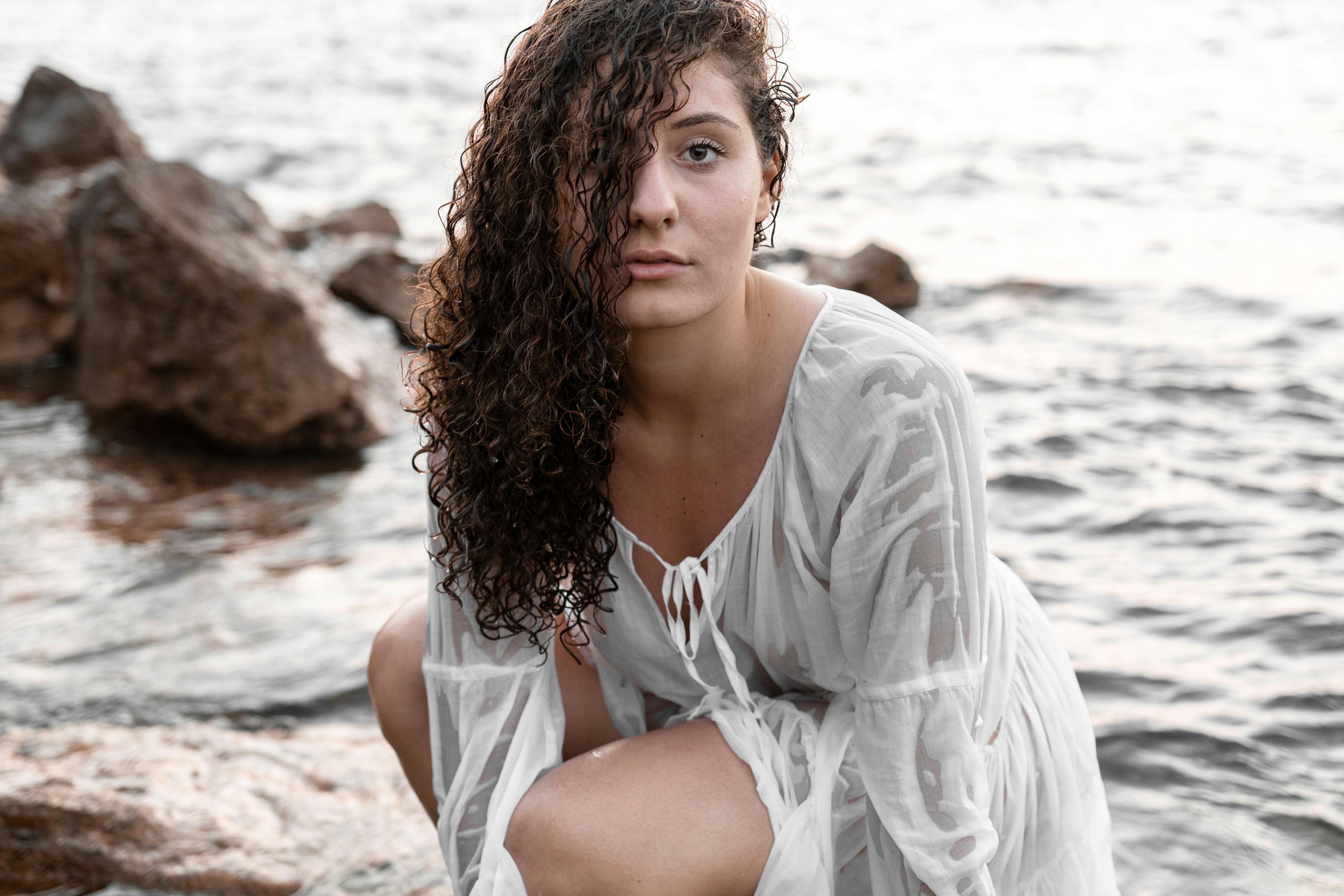 Woman Crouching On Rock Near Body Of Water · Free Stock Photo