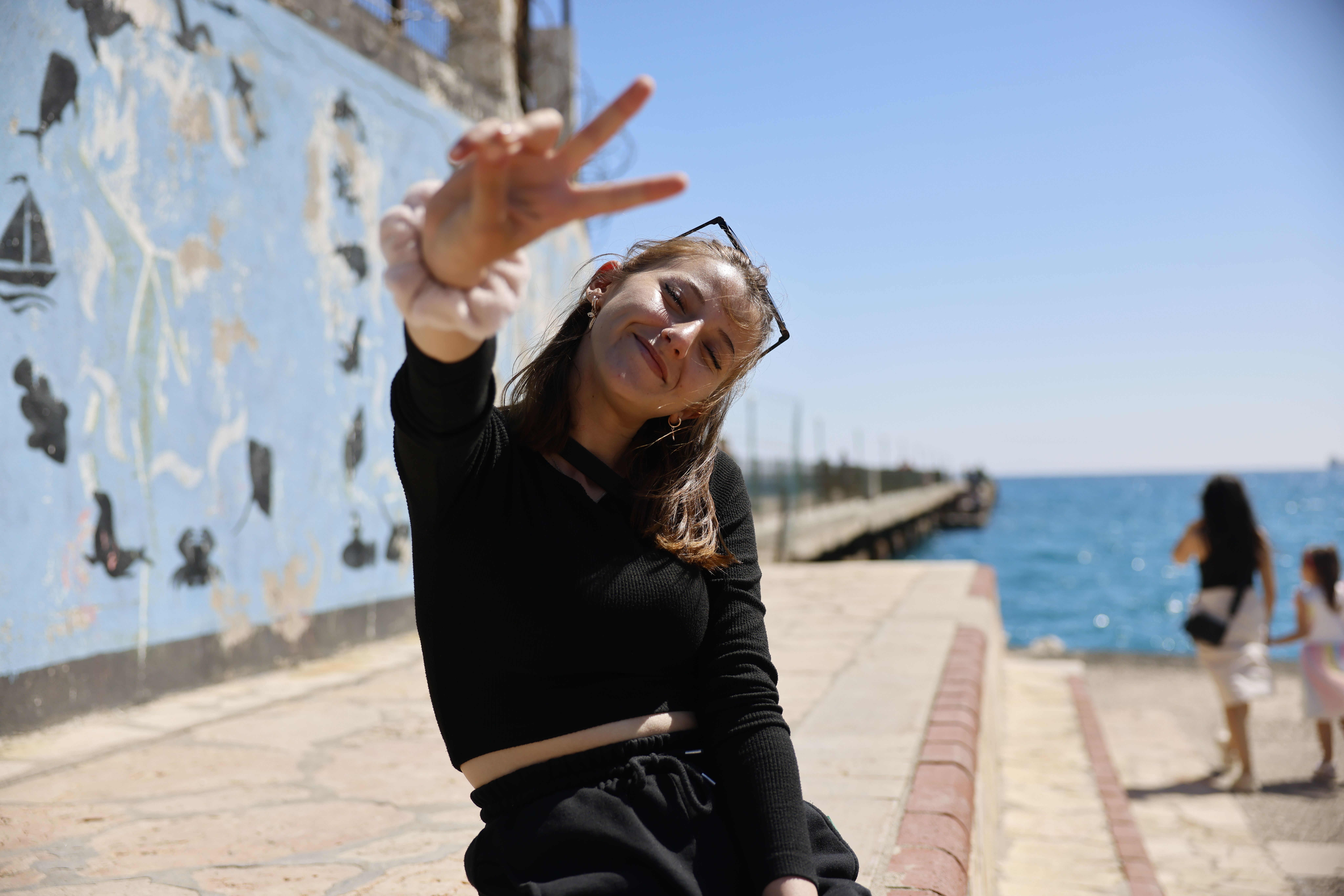 Young Woman Sitting on the Steps by the Sea and Showing Victory Gesture ...