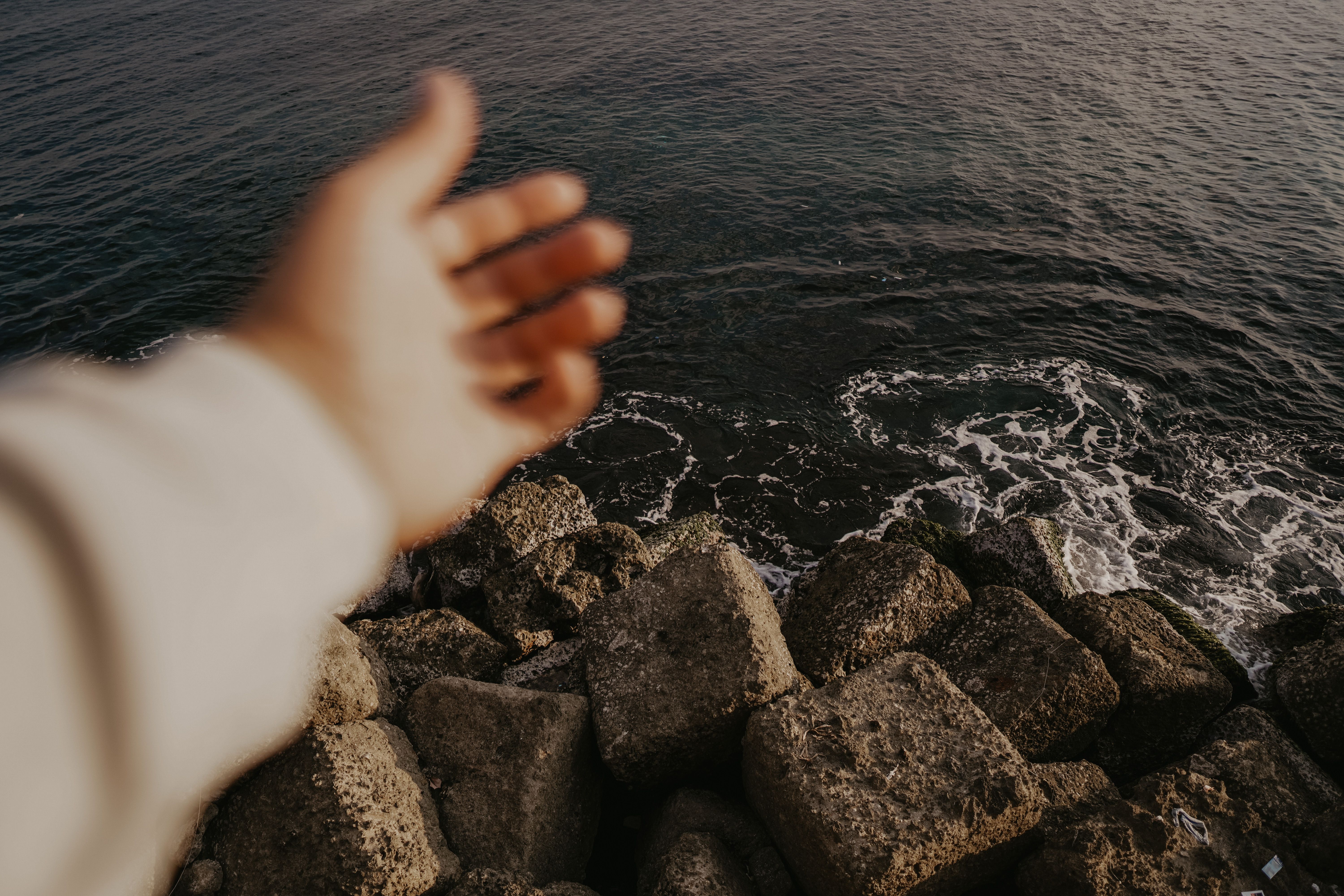 A person reaching out to the ocean with their hand · Free Stock Photo