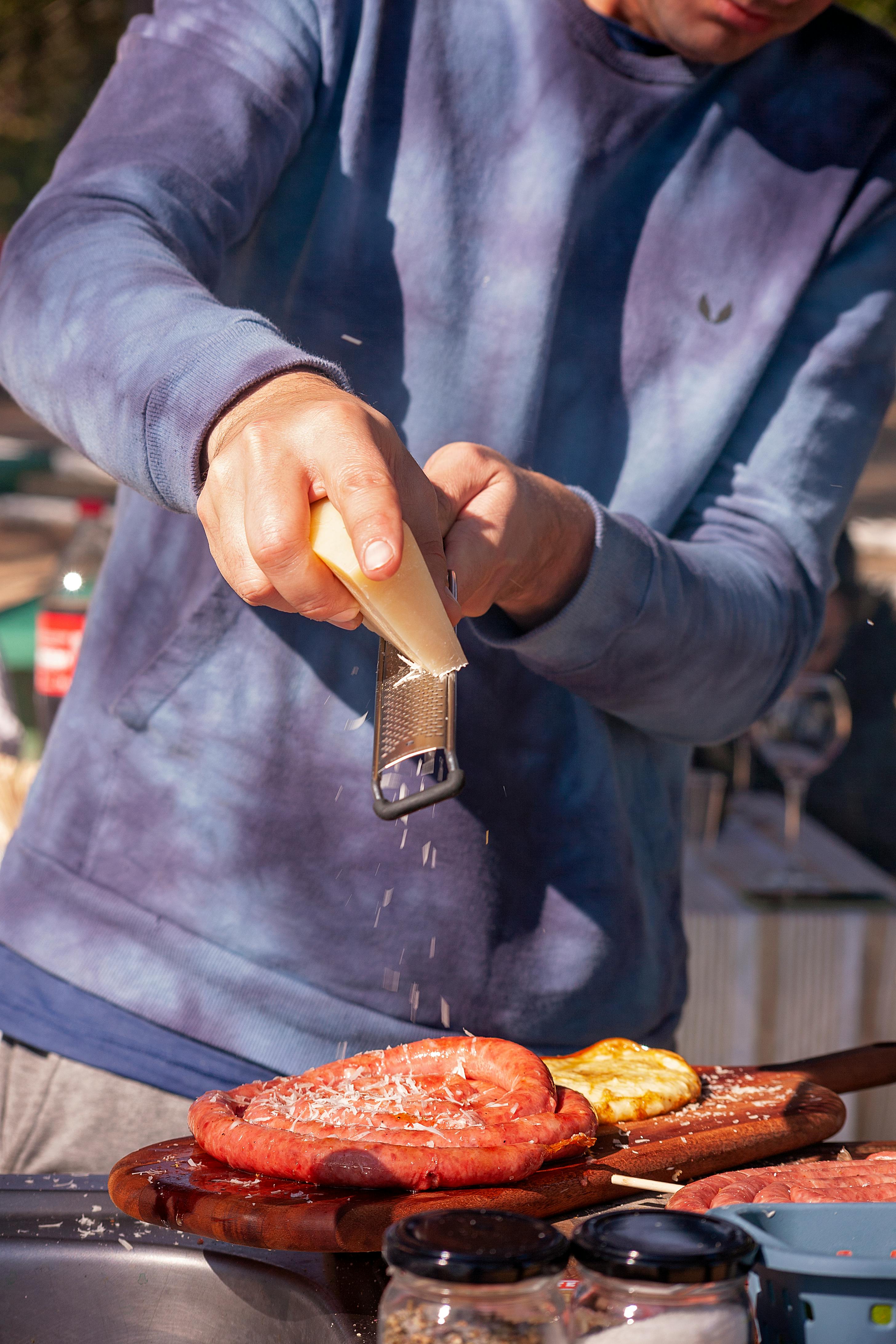 Man Grating Cheese on Sausage · Free Stock Photo