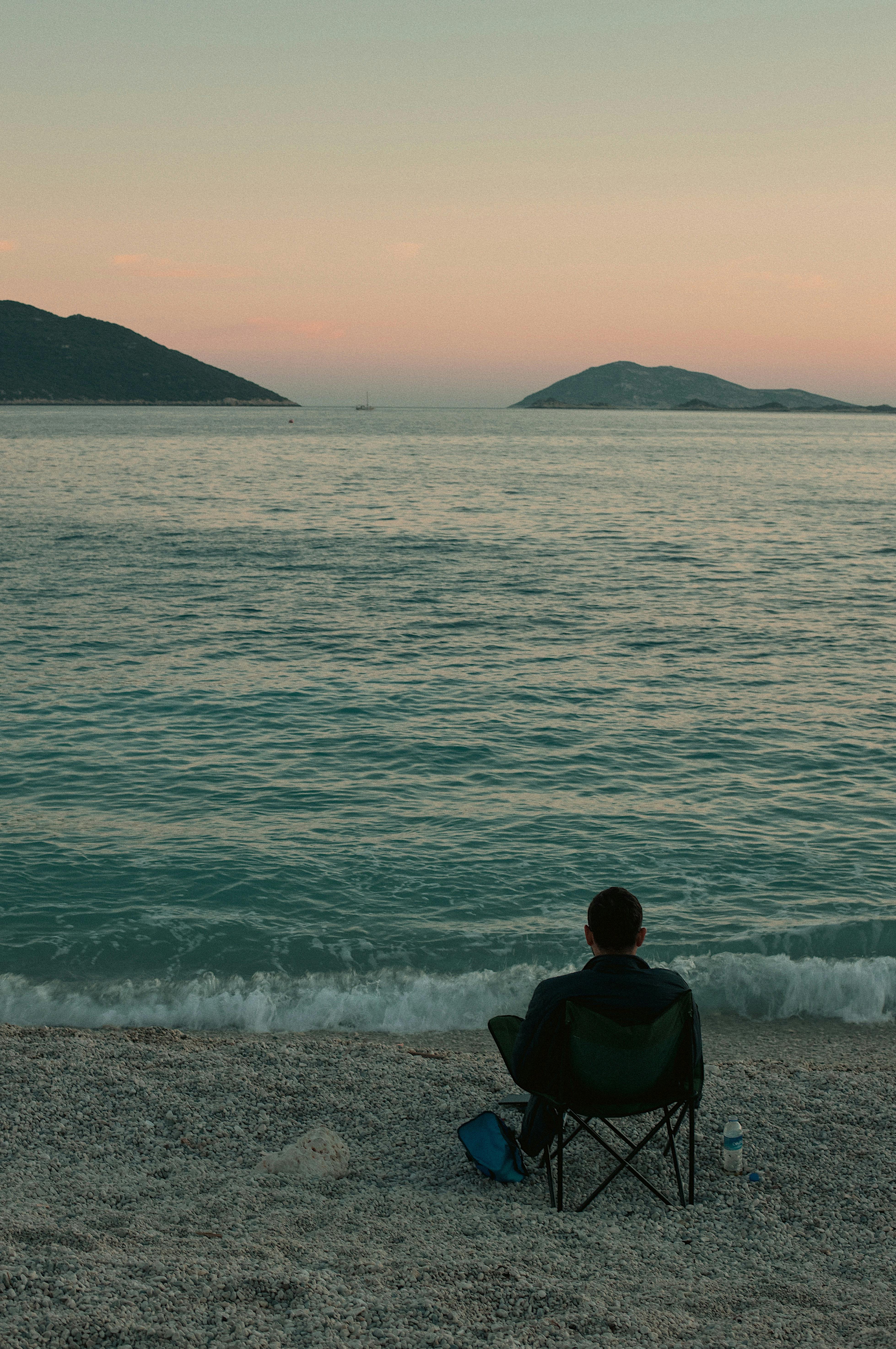 A man sitting in a chair on the beach at sunset · Free Stock Photo