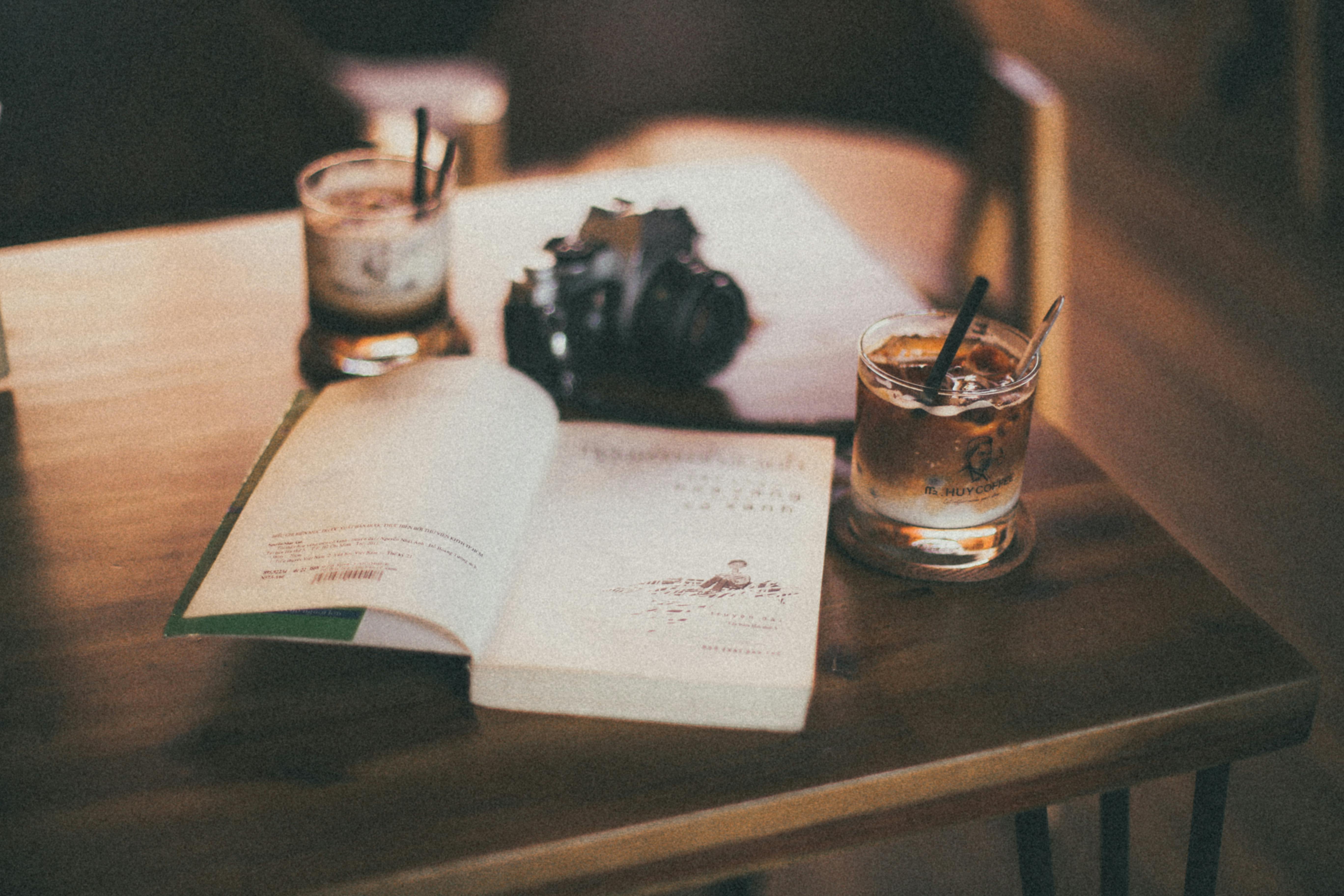 Filled Pint Glass Beside Camera and Book on Table · Free Stock Photo