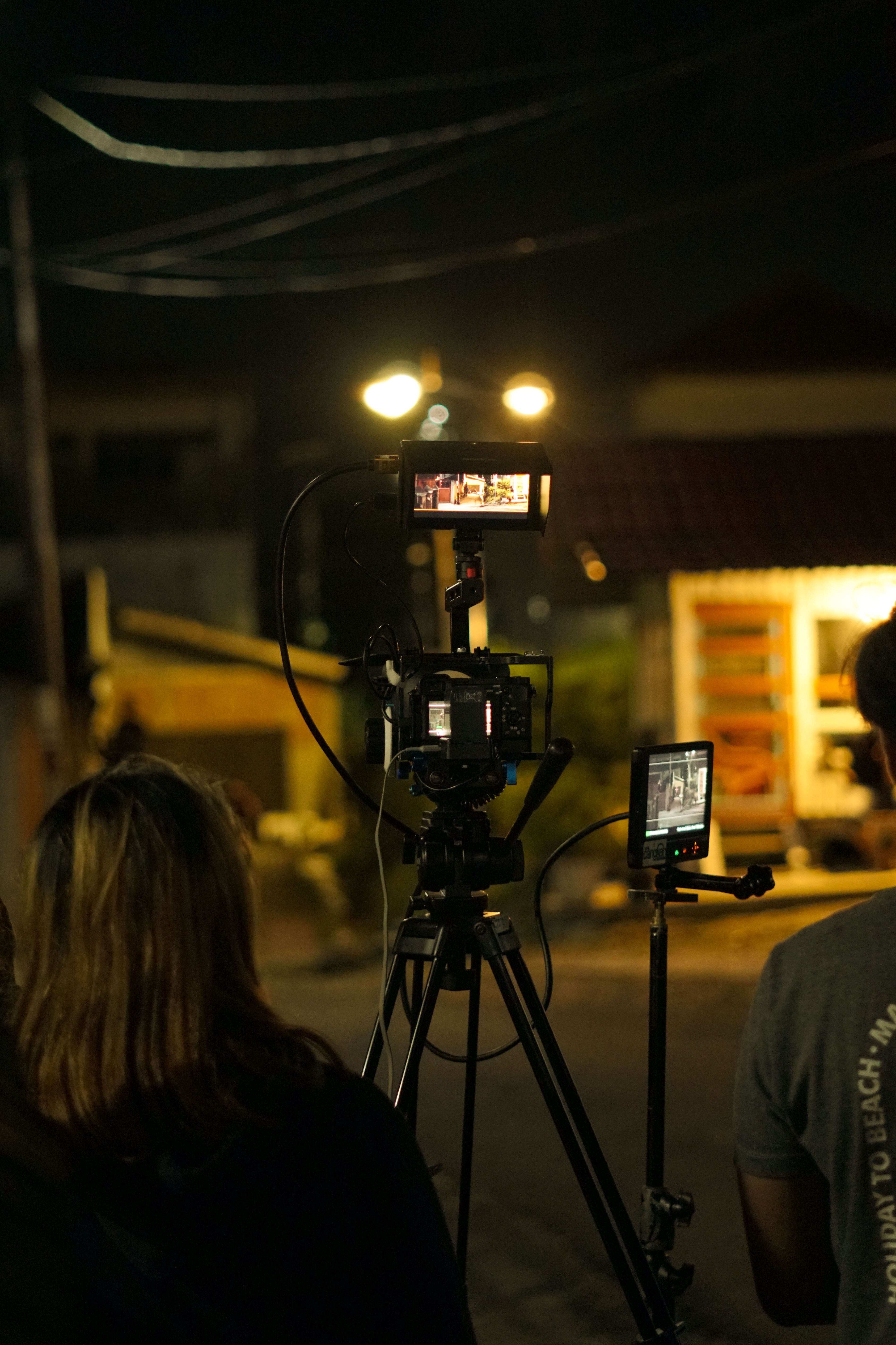 Two Videographers Filming a Night Street Scene with a Camera on Tripod ...