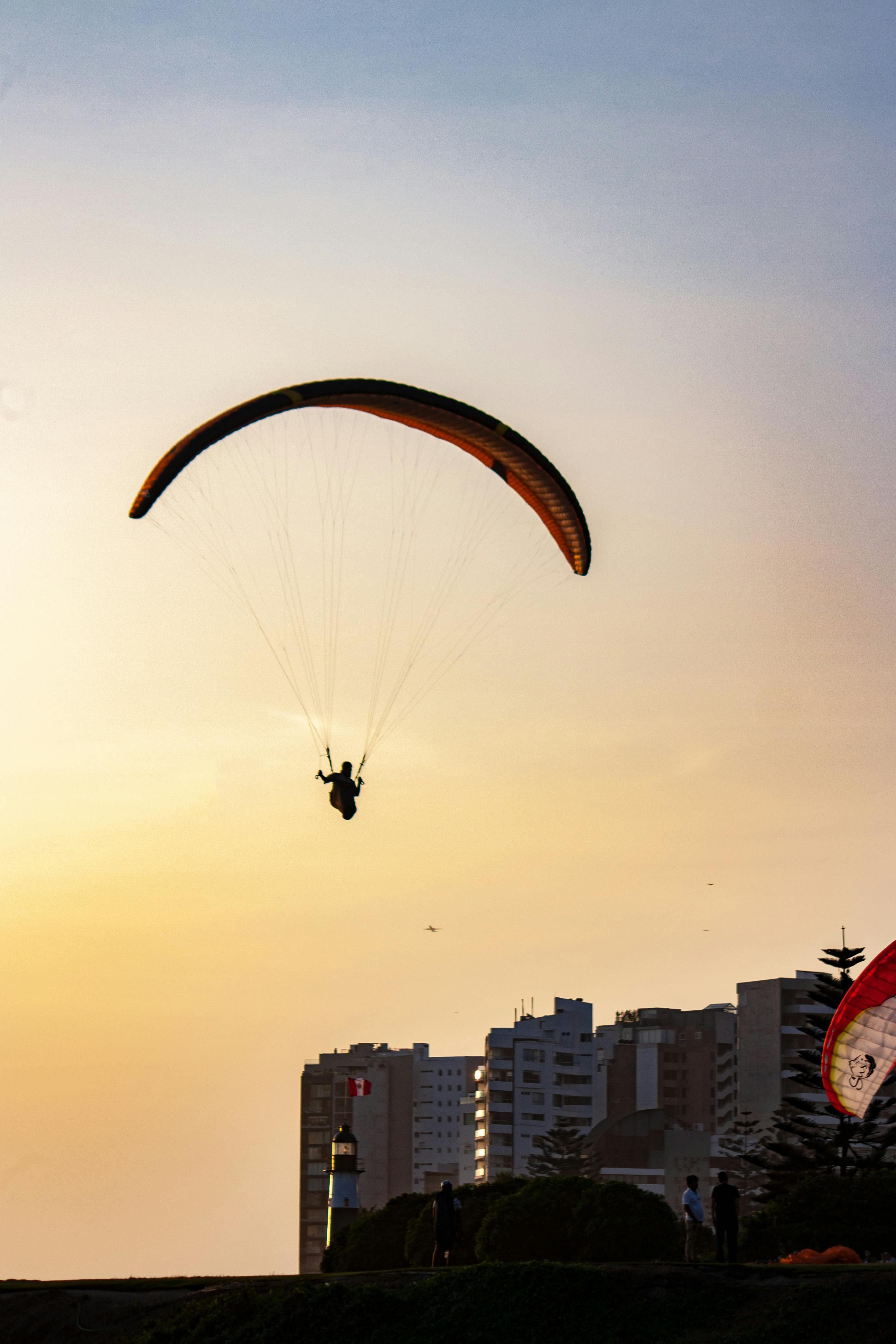 Person Parachuting over Town at Sunset · Free Stock Photo