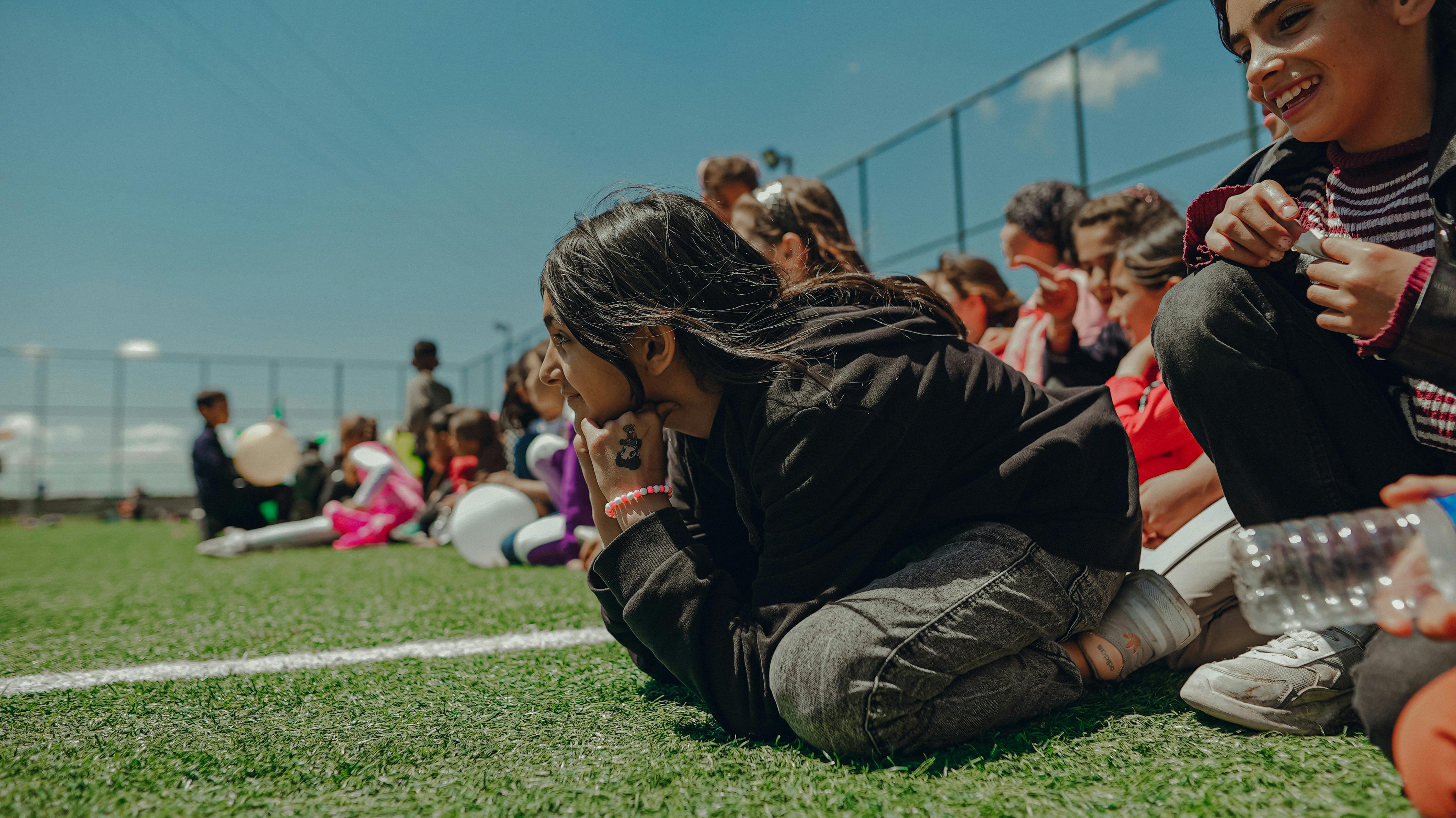 Smiling Girls Sitting on Football Field · Free Stock Photo