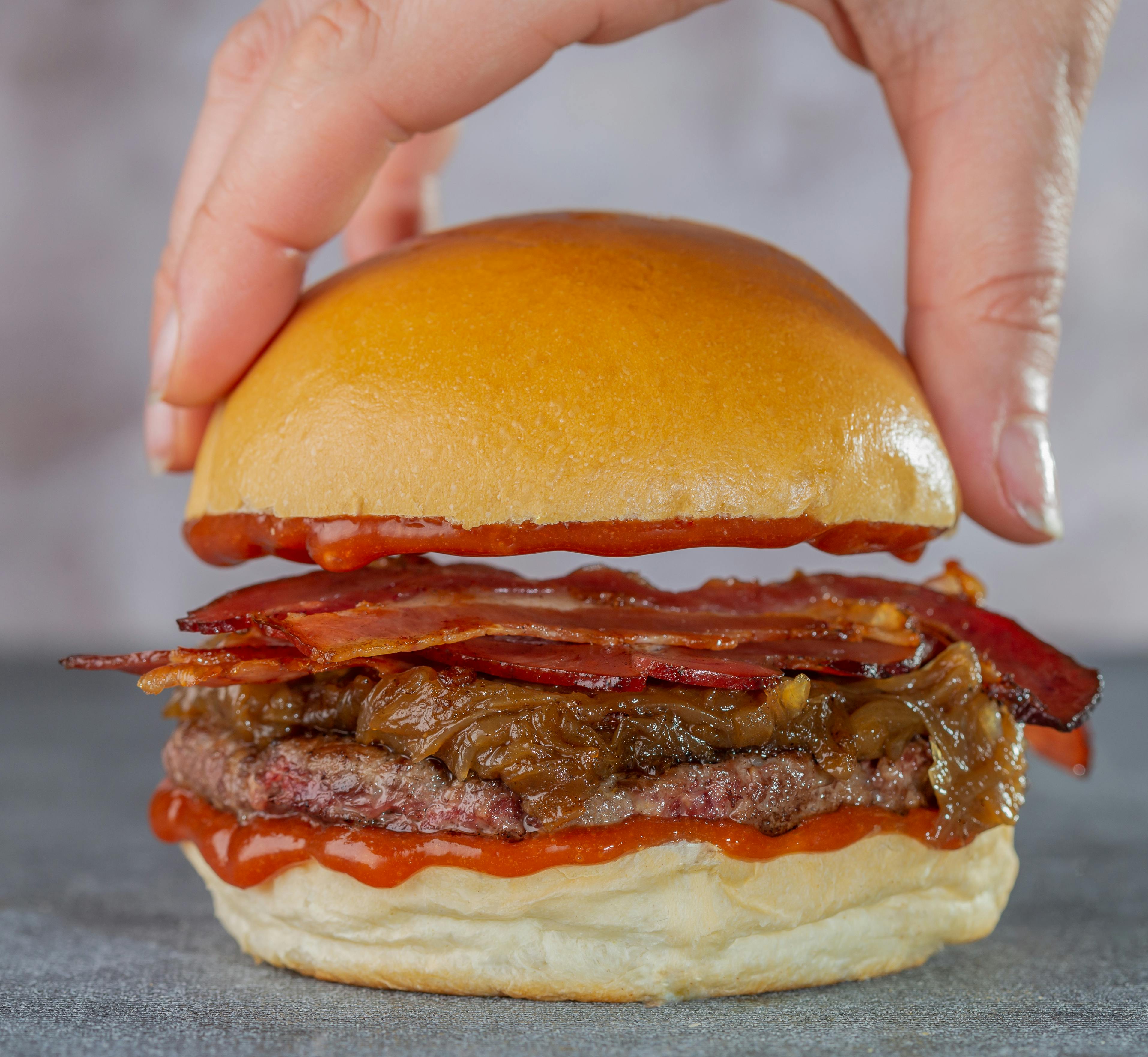 Photo of a Person's Hand Holding a Burger with Red Sauce · Free Stock Photo