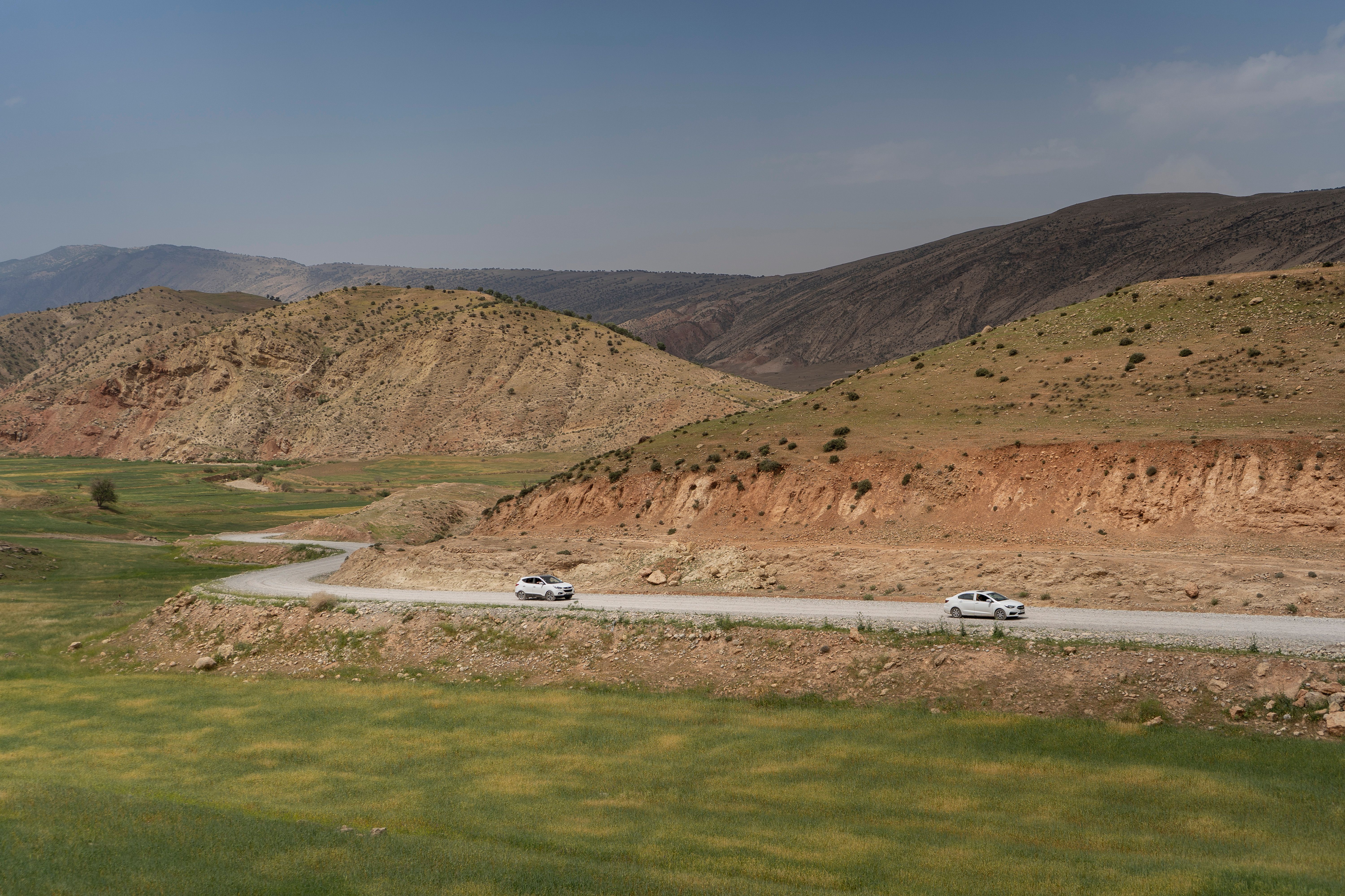Two Cars Driving along a Winding Road with Hills in the Background ...