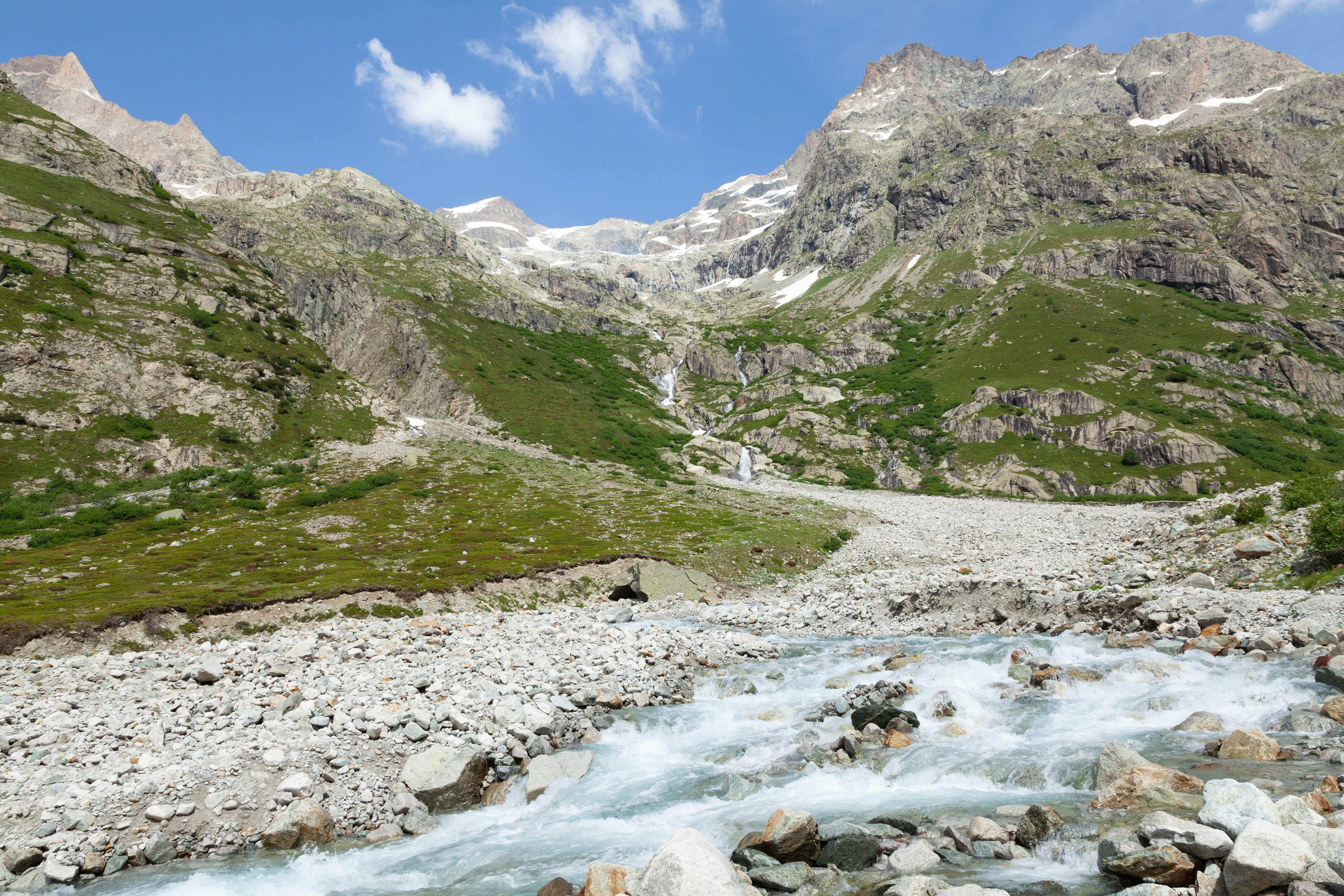 A river flowing through a rocky valley with mountains in the background ...