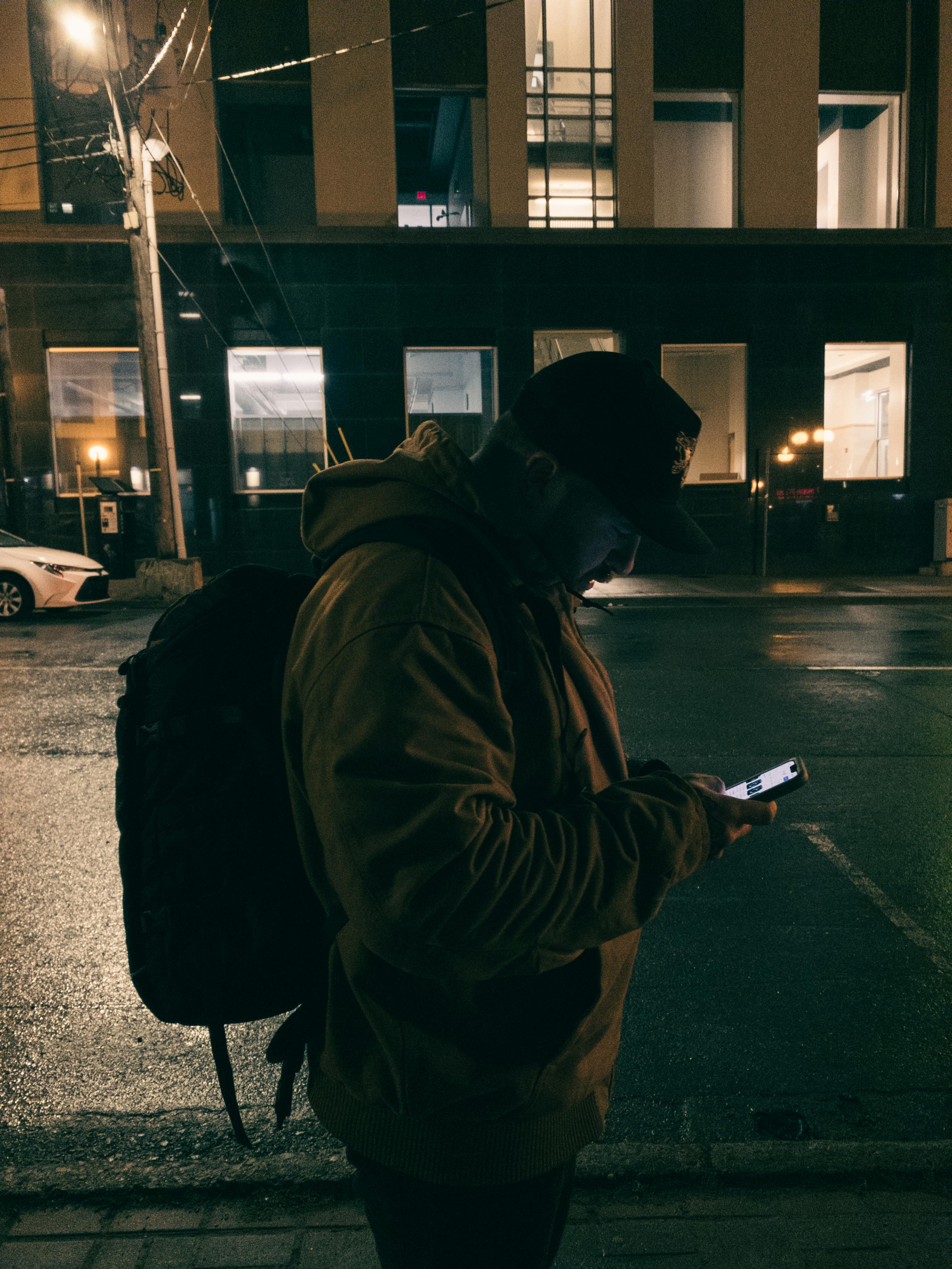 Man with Backpack Standing on Street at Night and Looking at Cellphone ...