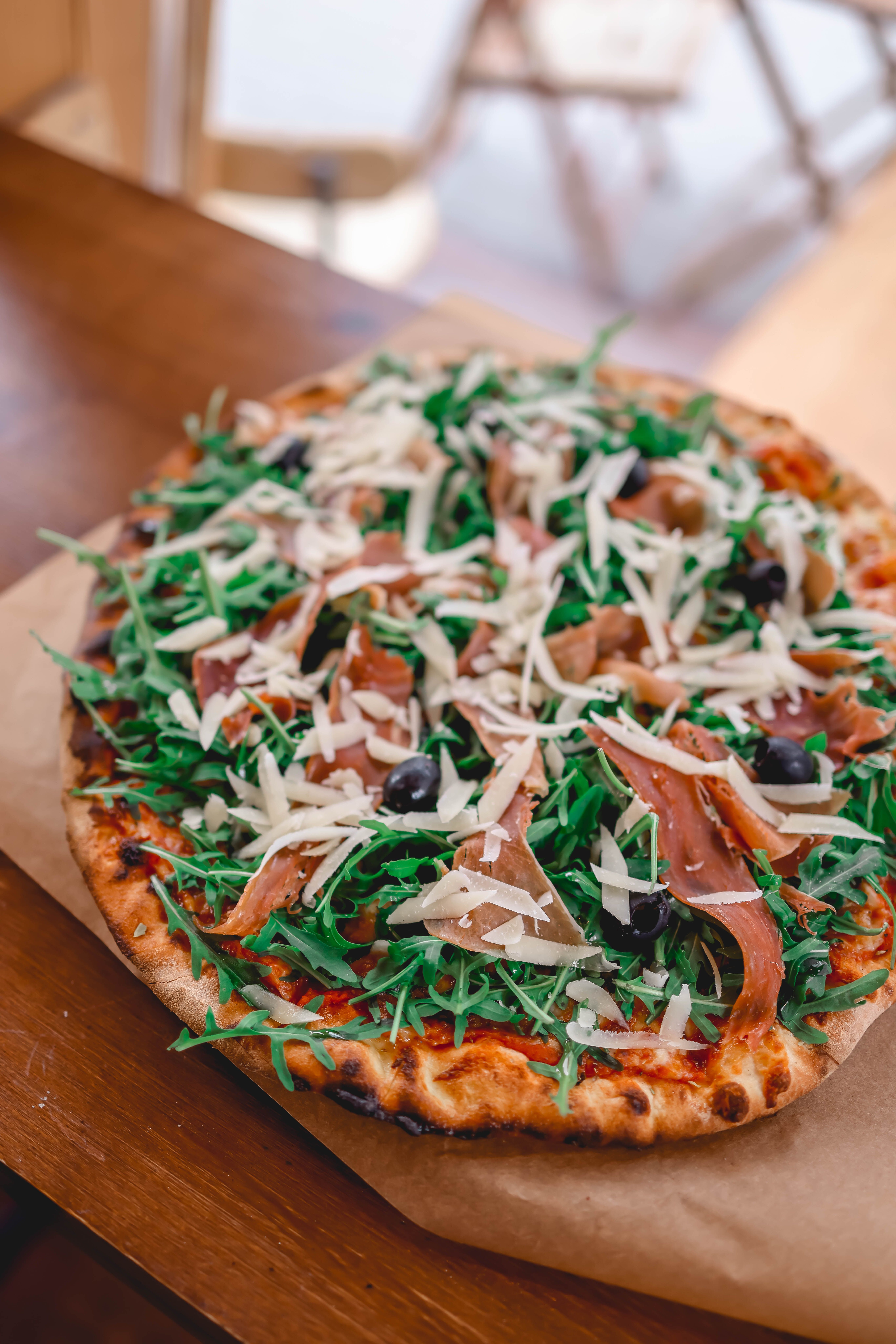 Pizza with Dry Curled Ham and Rucola on a Wooden Table · Free Stock Photo