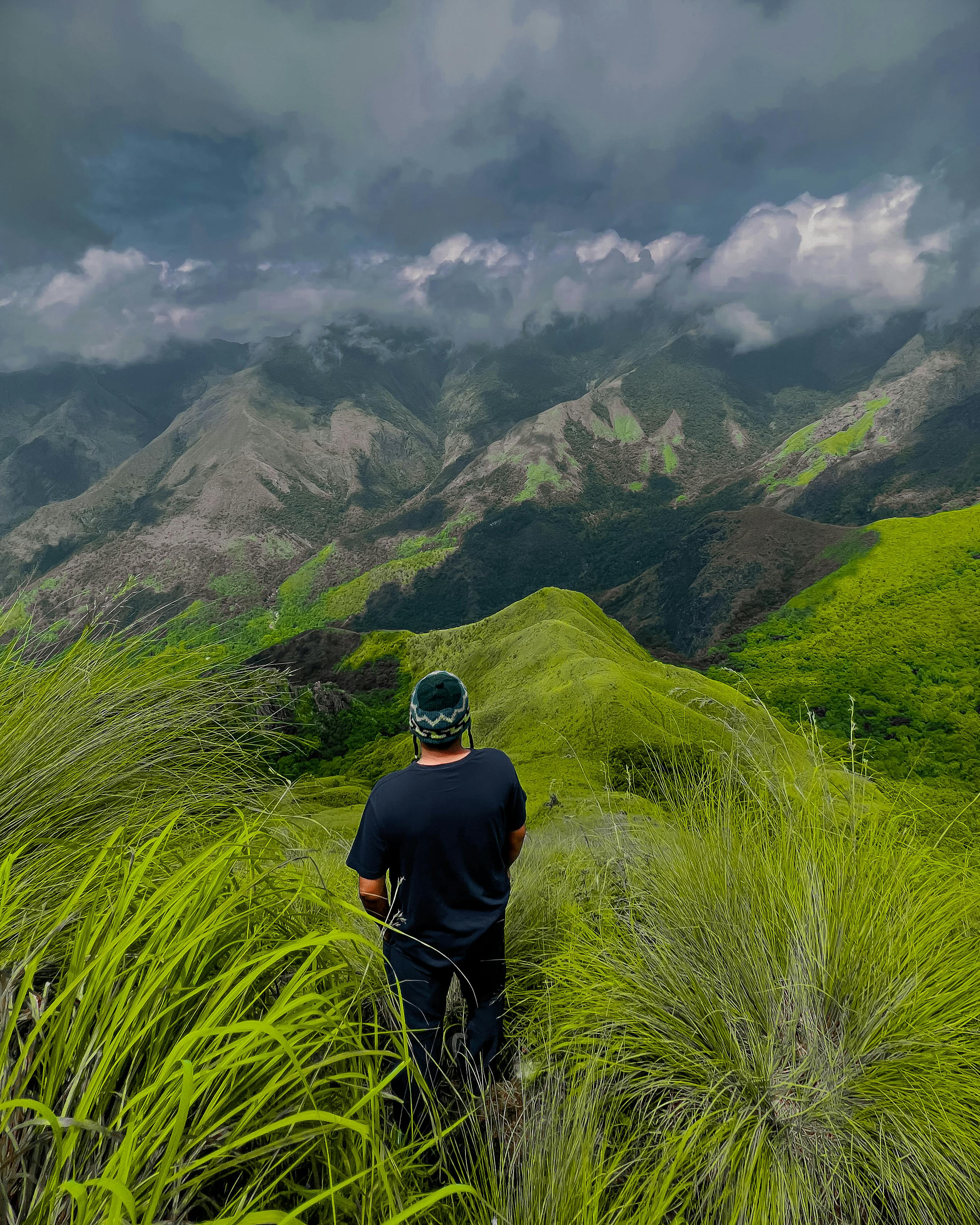 Man Standing atop Green Peak Overlooking Mountain Valley · Free Stock Photo