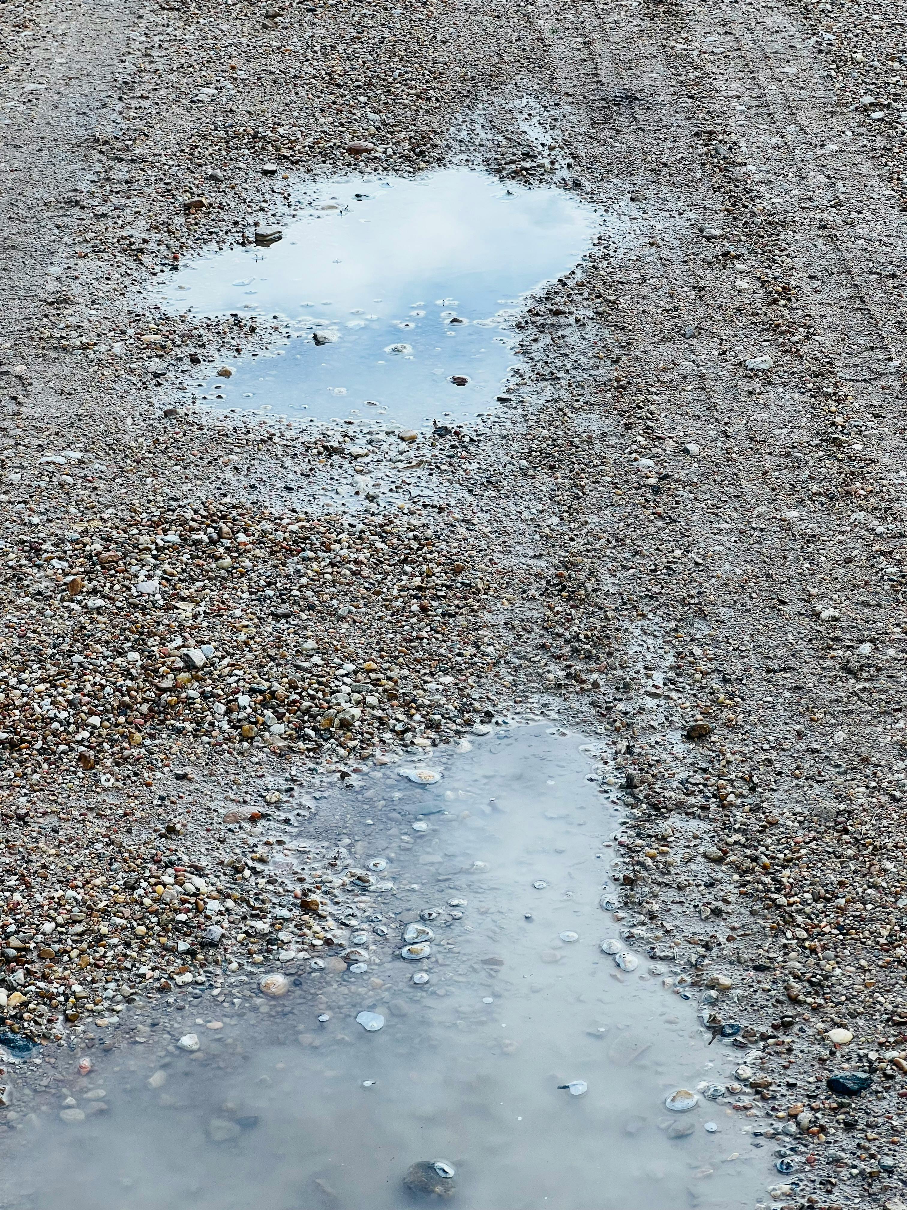 A puddle of water on a gravel road · Free Stock Photo