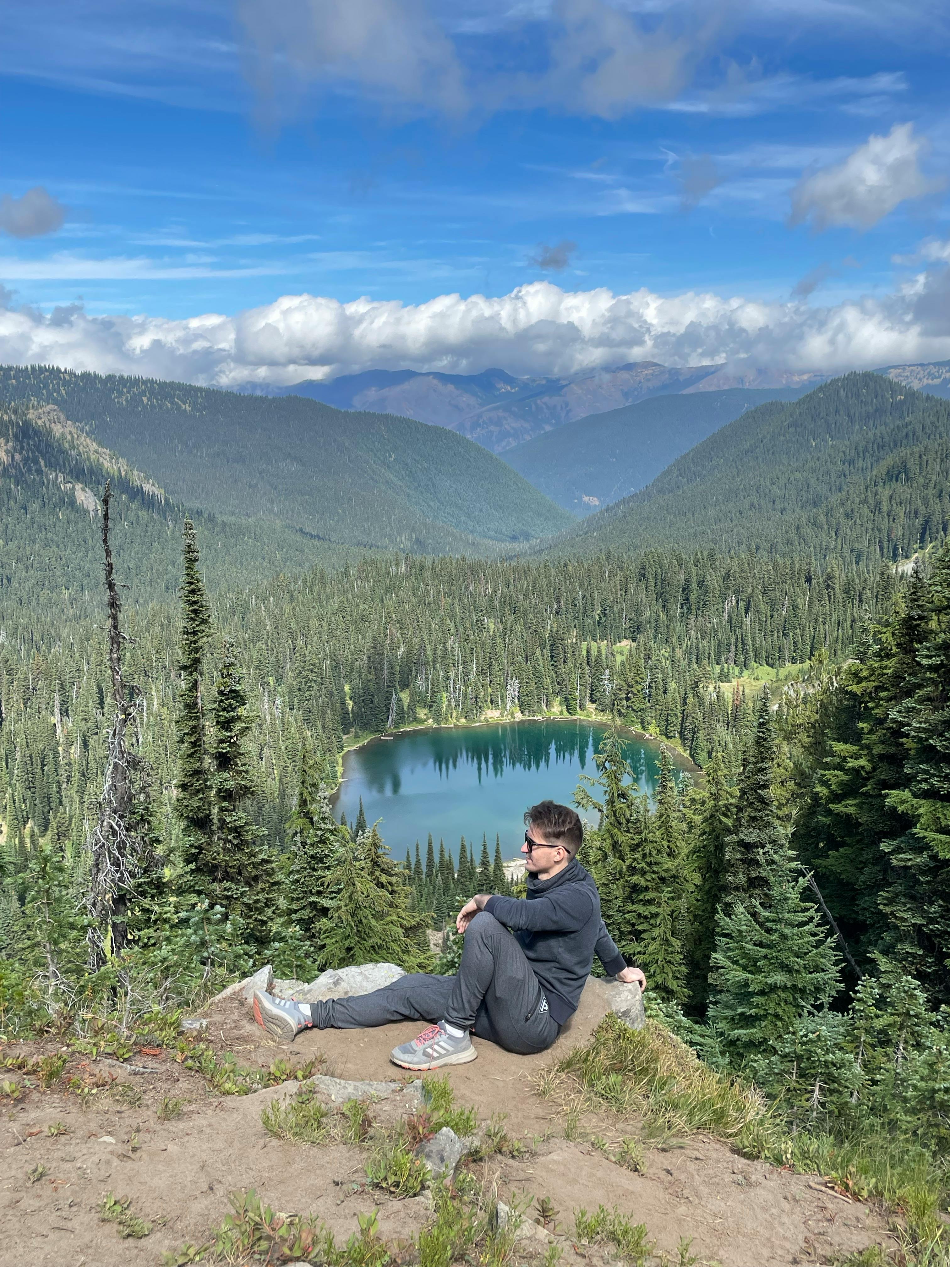 Young Man Sitting on a Mountain Peak with the View of the Lake in the ...