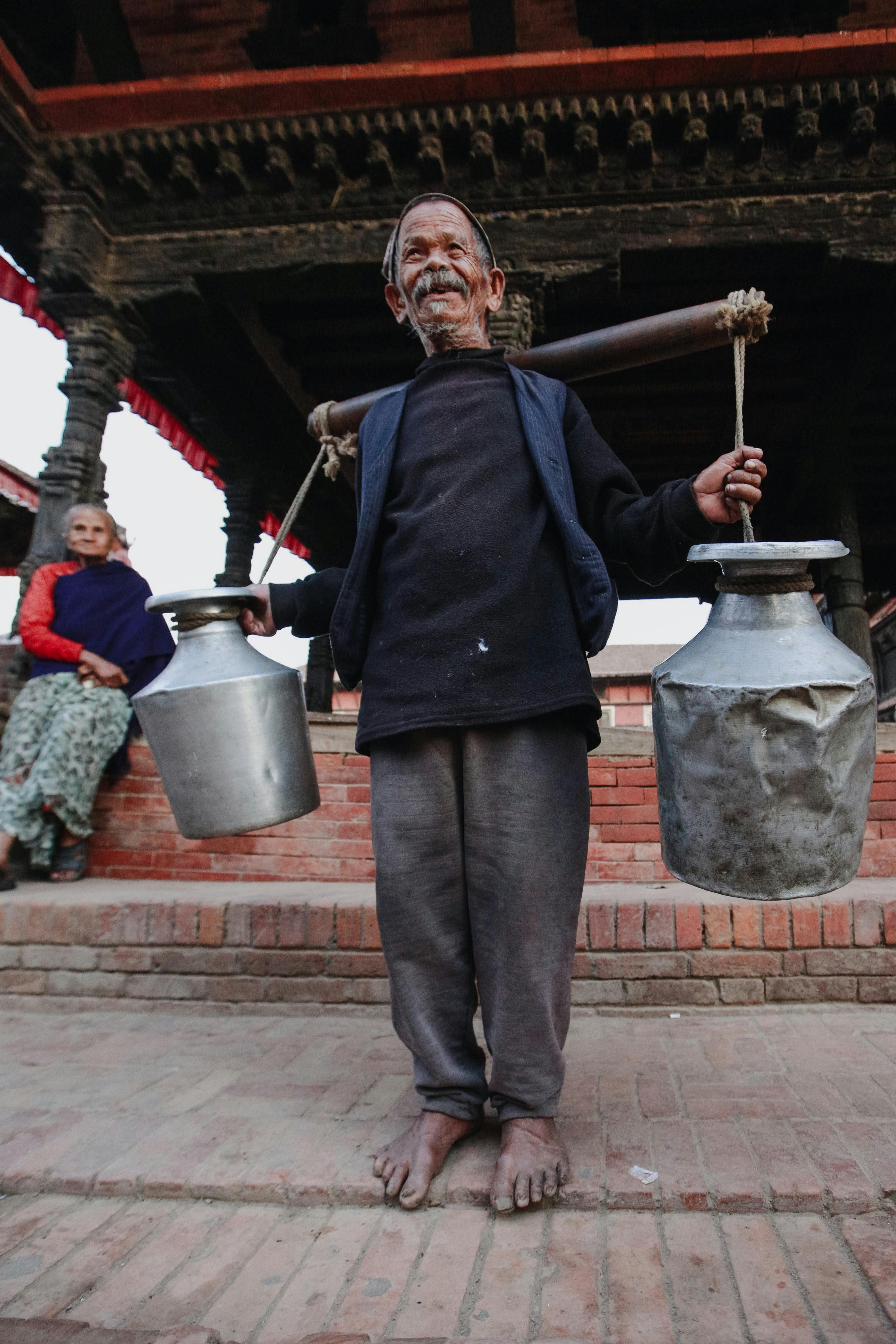 Barefoot Elderly Man Carrying Metal Tanks · Free Stock Photo