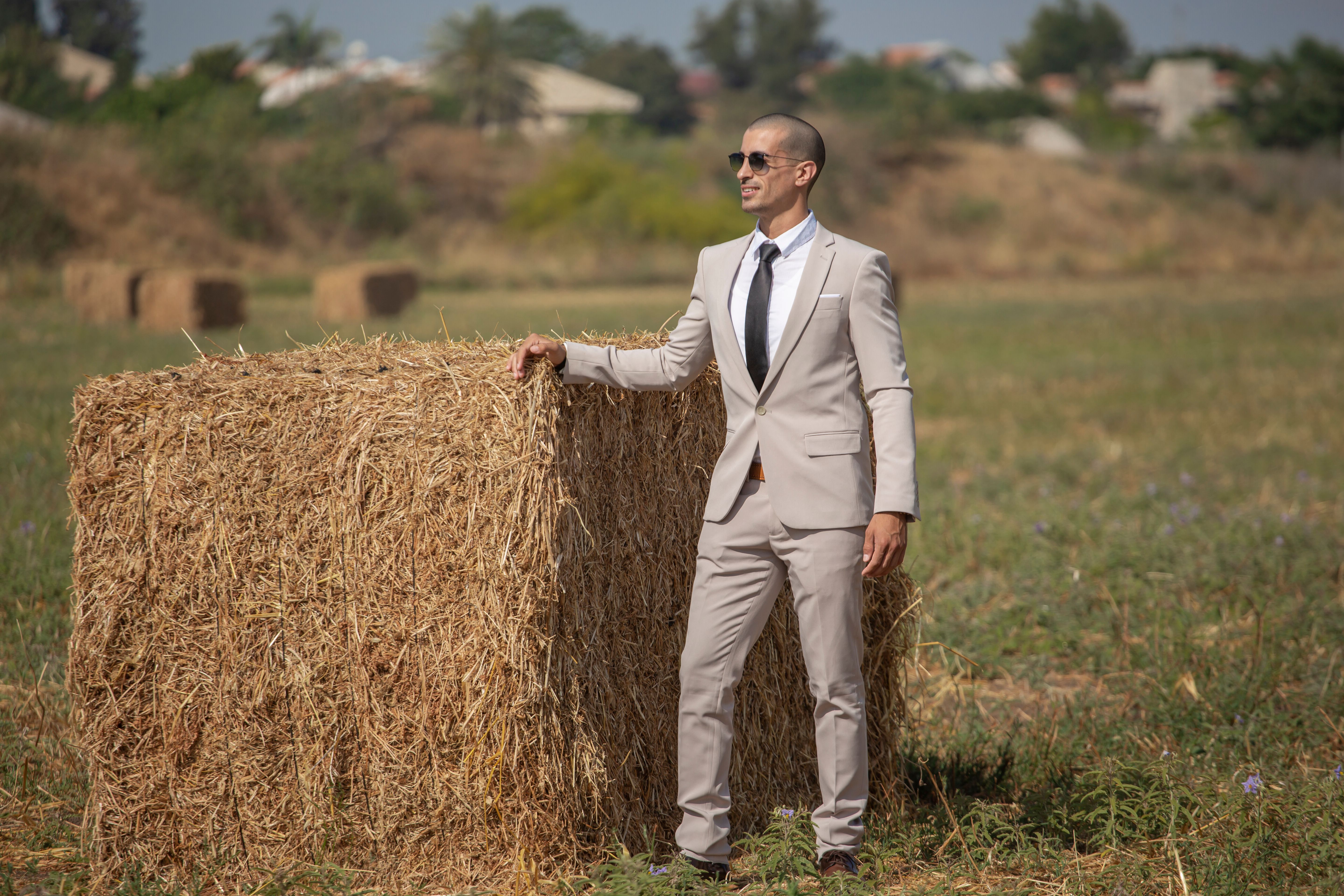 A man in a suit and tie standing next to a pile of hay · Free Stock Photo