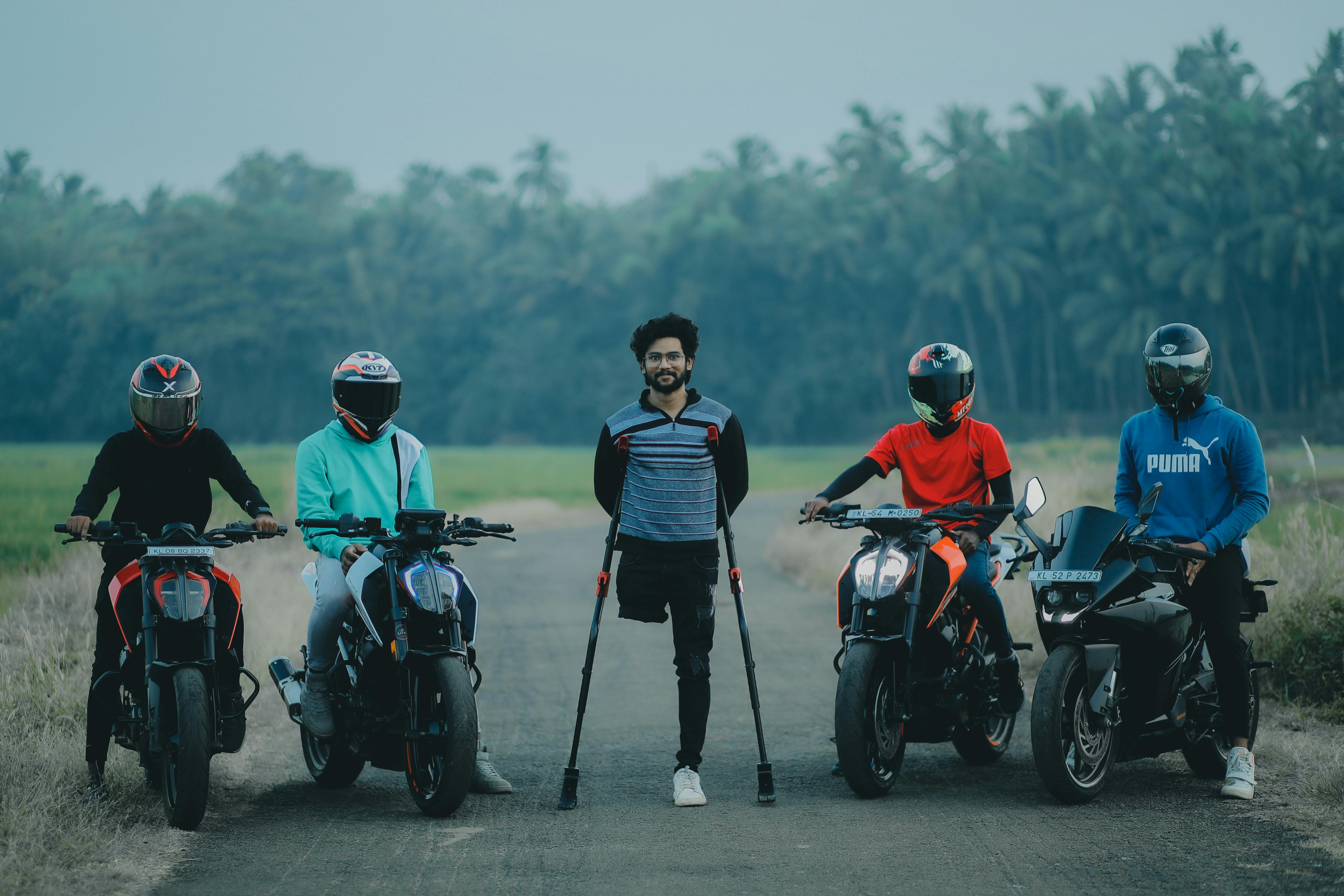 Amputee Standing between Friends Sitting on Motorcycles · Free Stock Photo