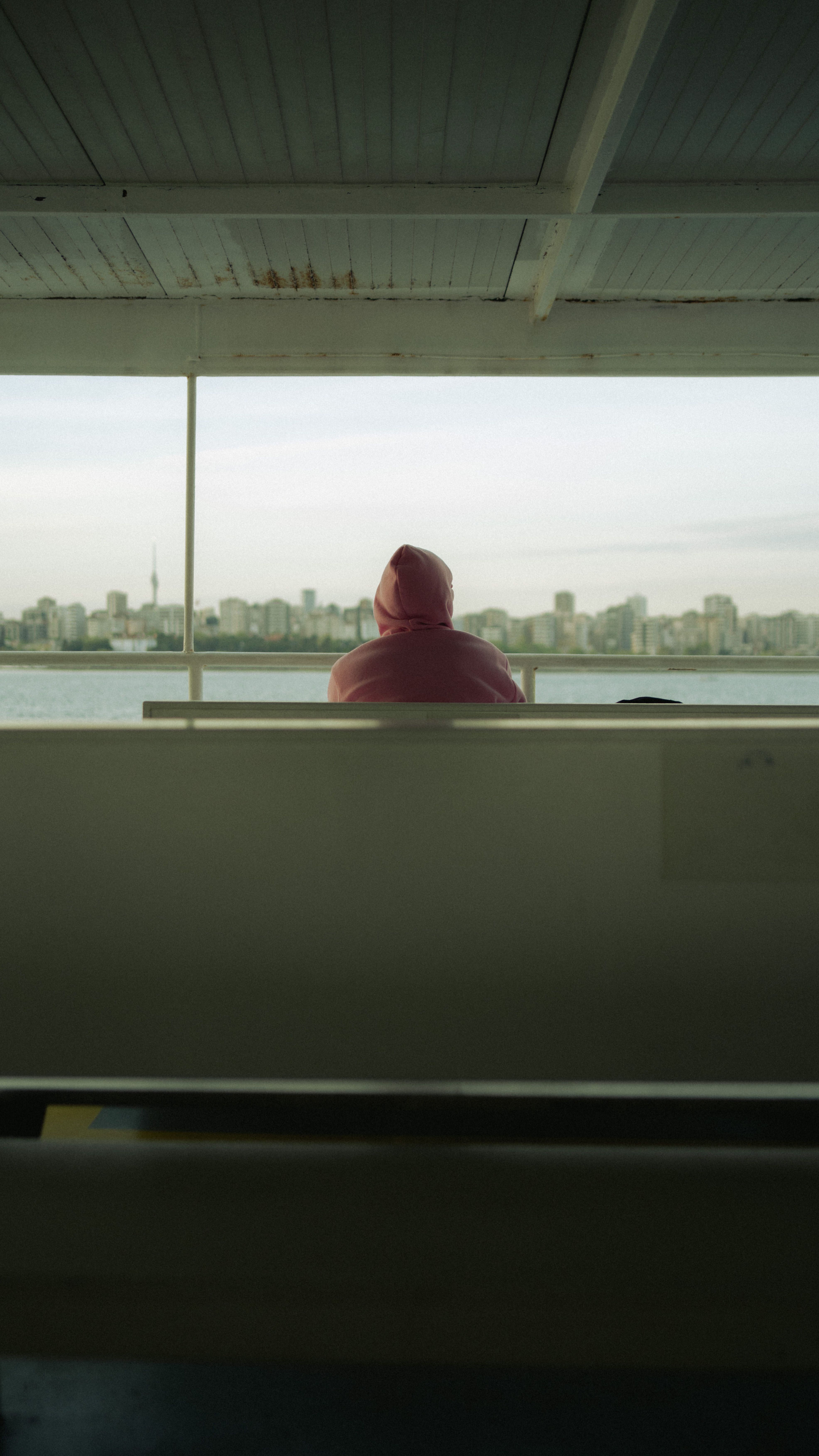 Back View of a Man Wearing a Hood, Sitting on a Ferry and Looking at ...