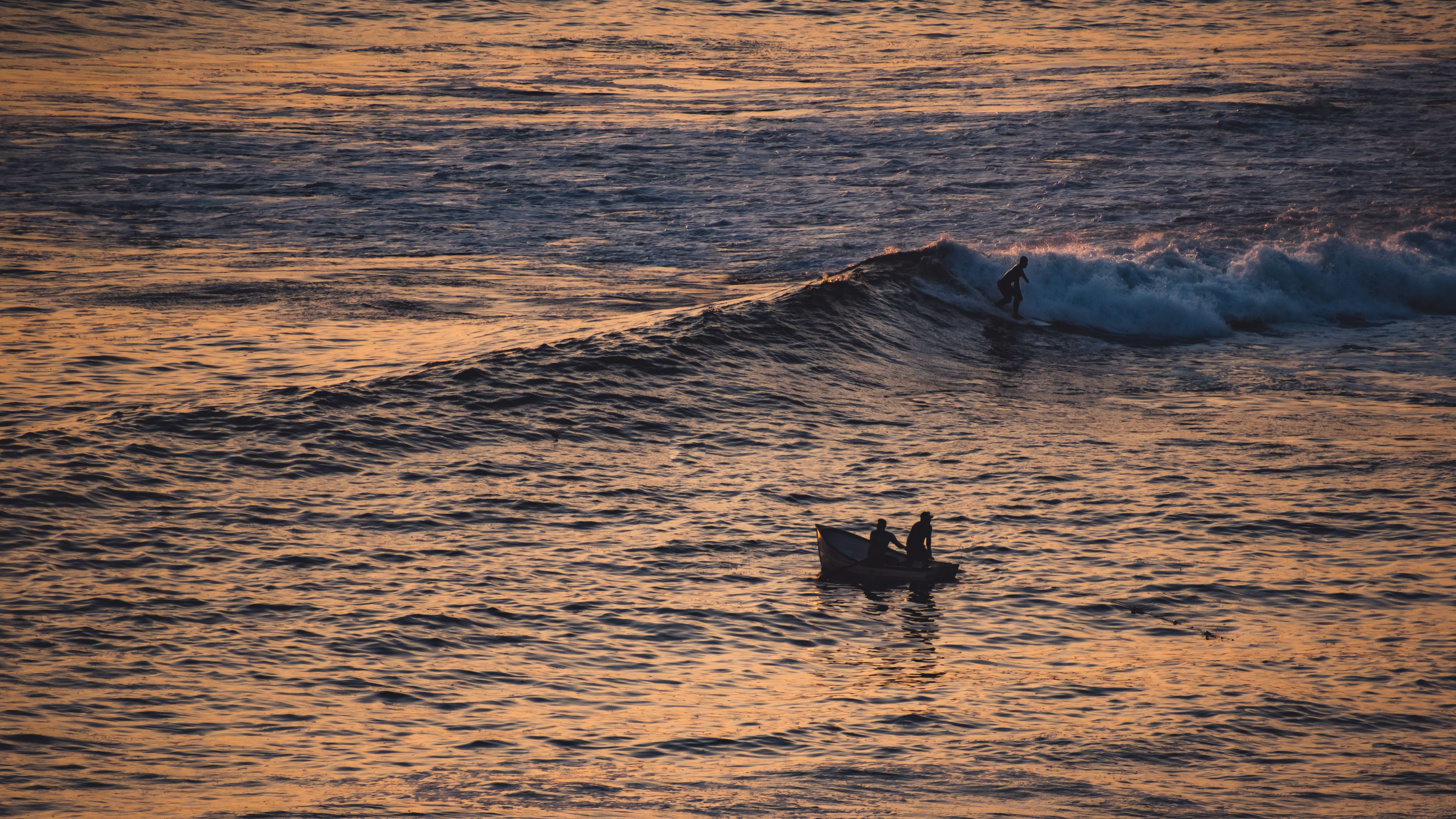 Silhouettes of People in a Boat and Surfing near the Shore at Sunset ...