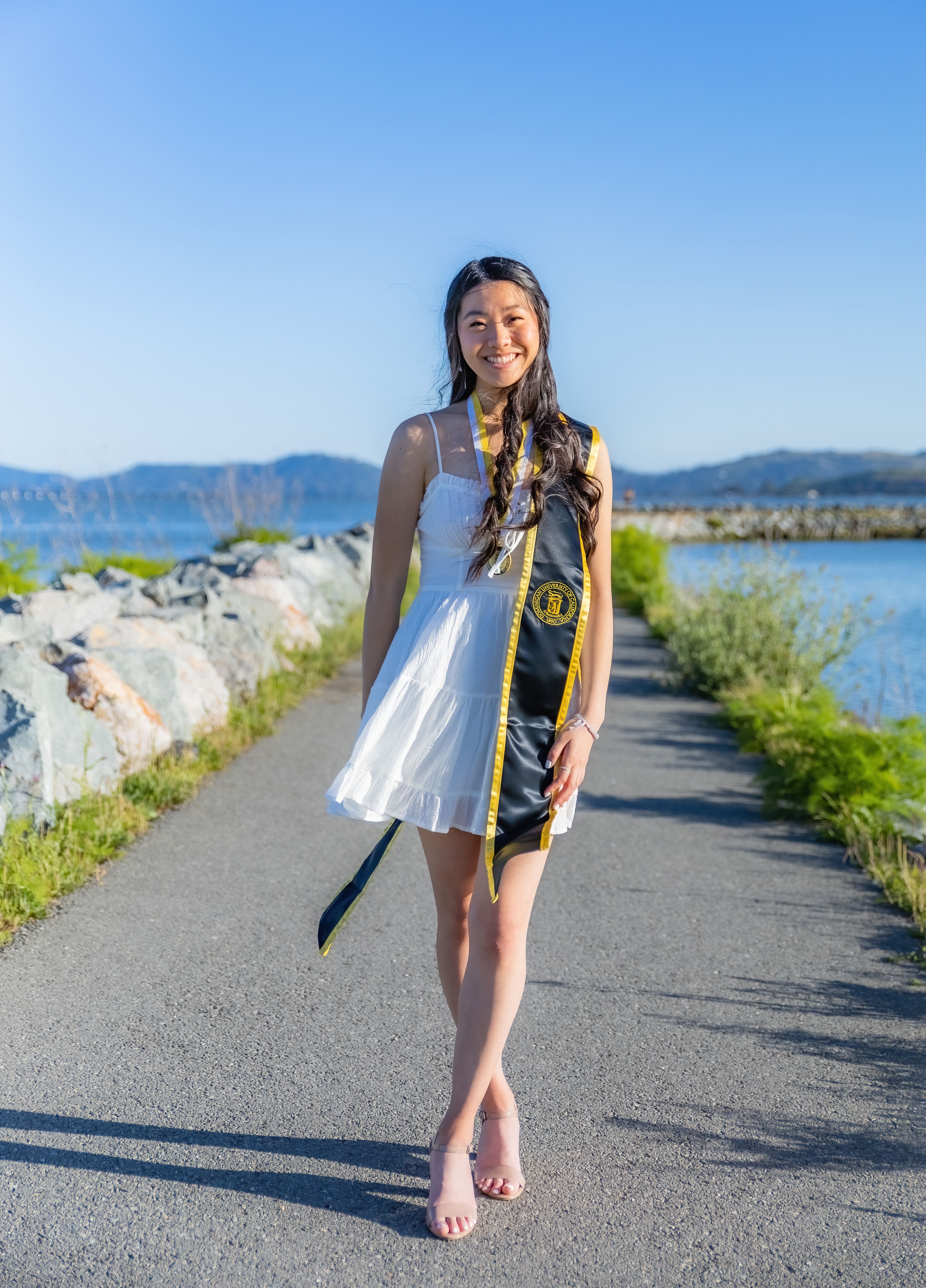 Smiling Woman in White Dress and Sash Standing on Sidewalk by Lake ...