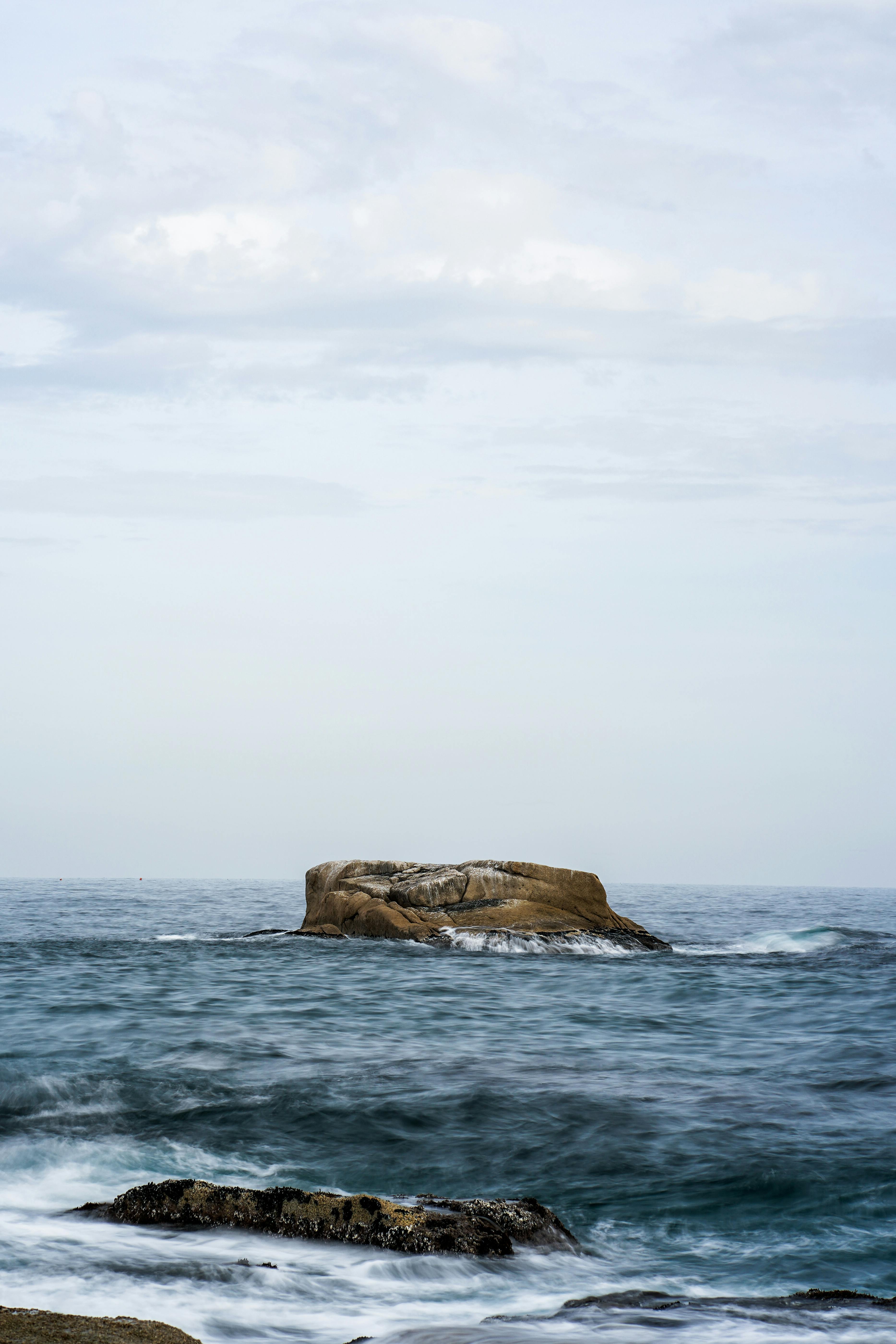 Rocky Cliff Near Calm Sea Under Gray Cloudy Sky · Free Stock Photo