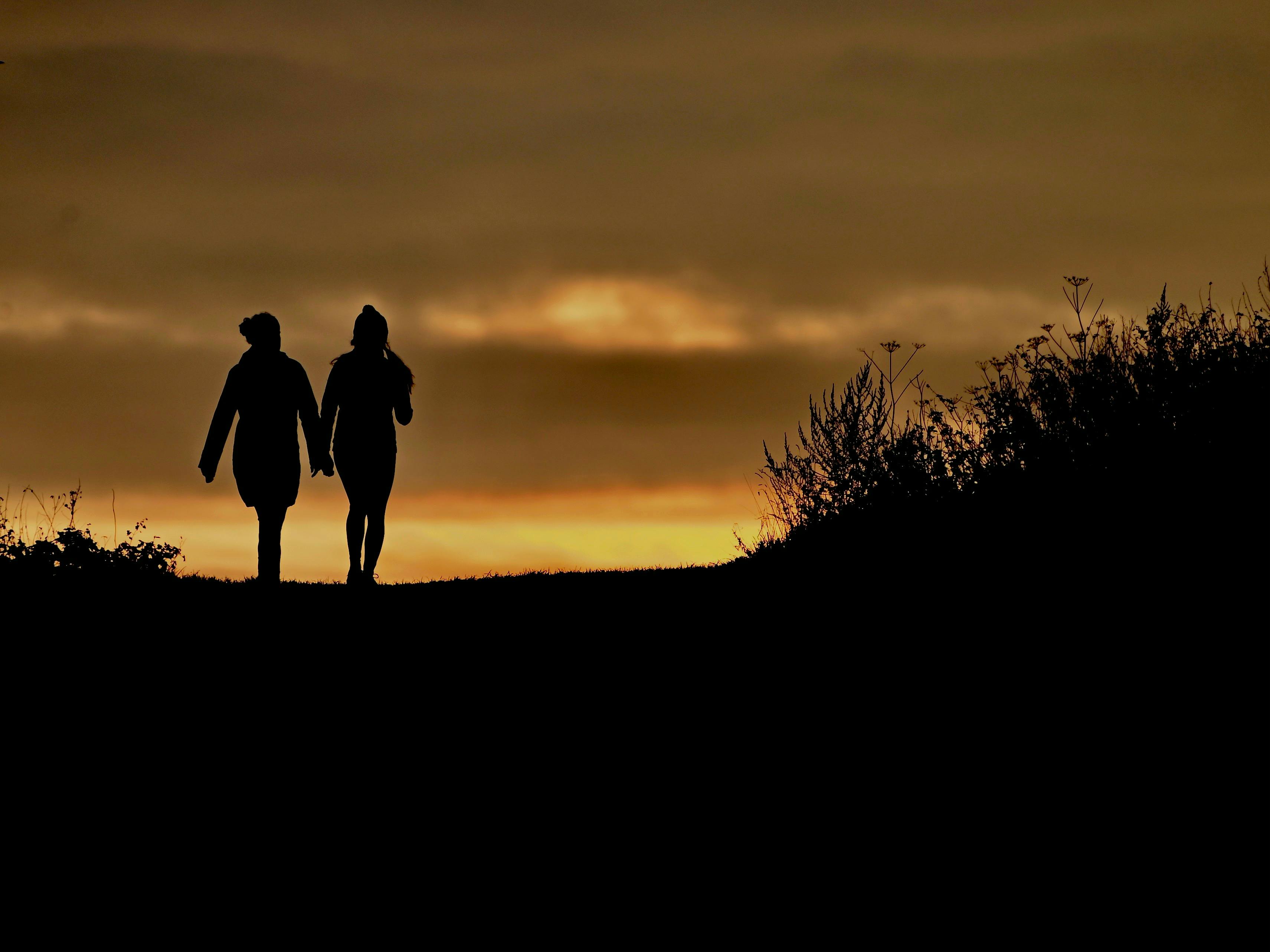Two people walking on a hill at sunset · Free Stock Photo