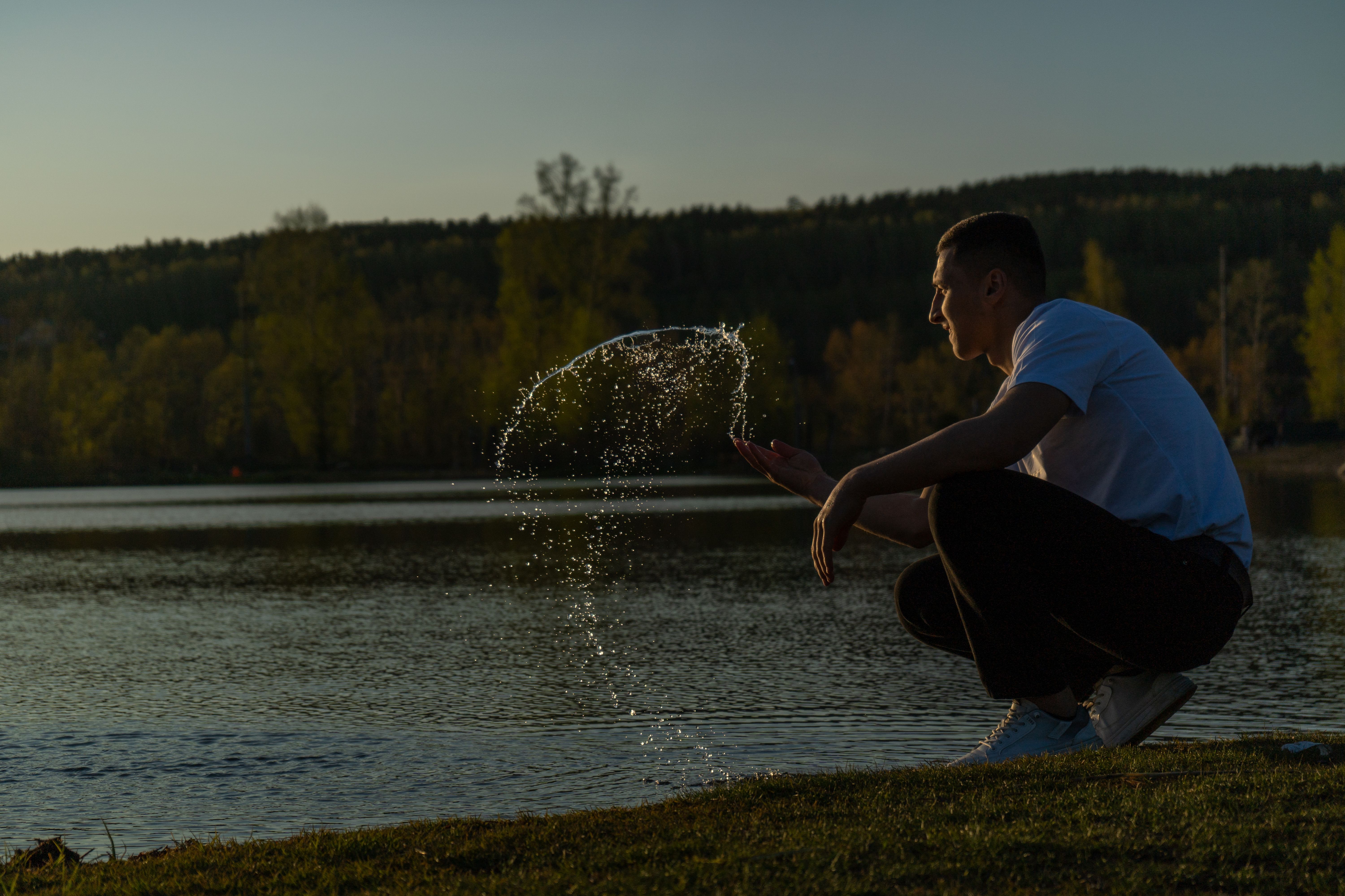 Man Squatting on Lakeshore and Splashing Water · Free Stock Photo