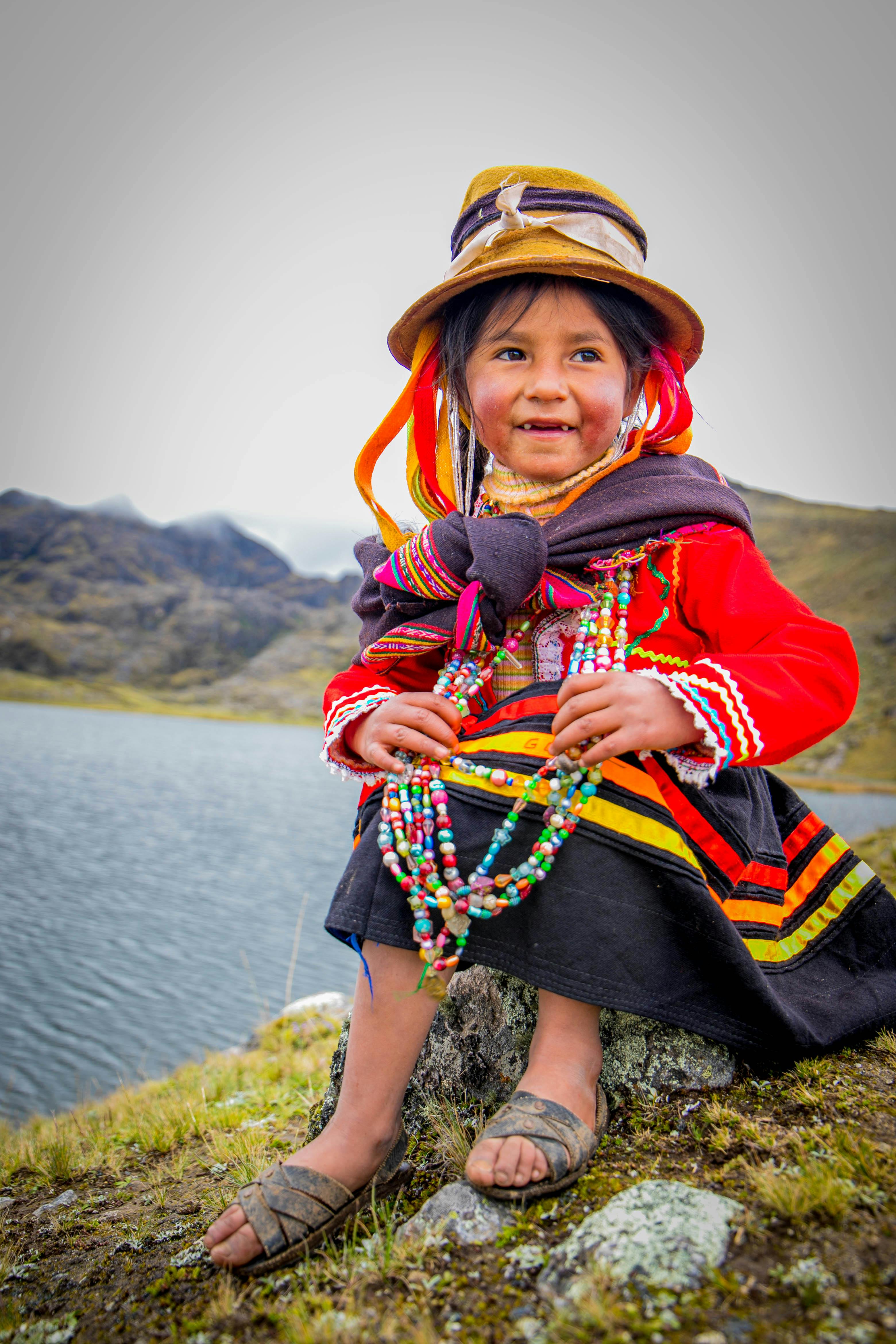 Girl in Peruvian Traditional Clothing Sitting by Lake · Free Stock Photo