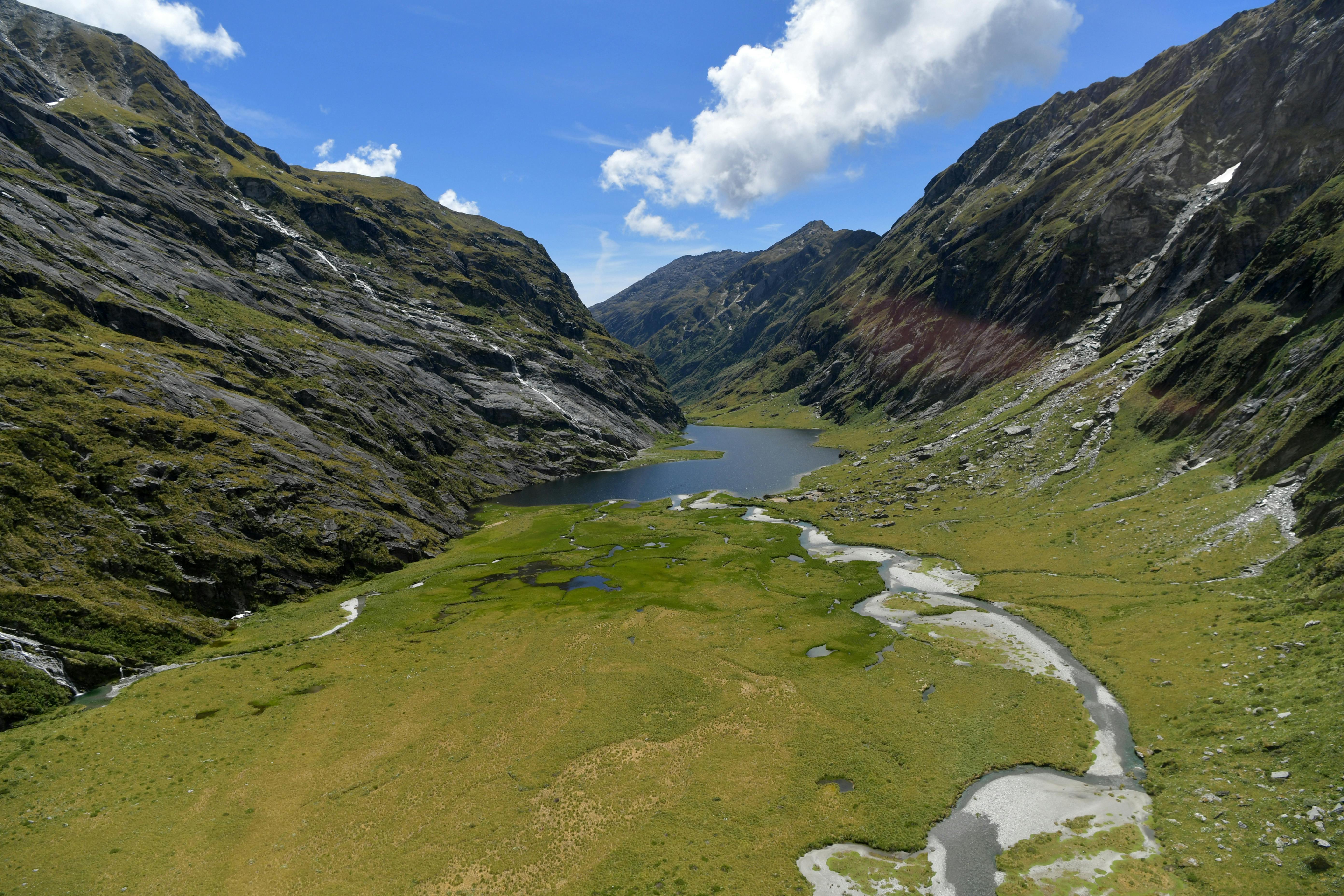 Green Field Island in the Middle of Body of Water Near Mountains during ...