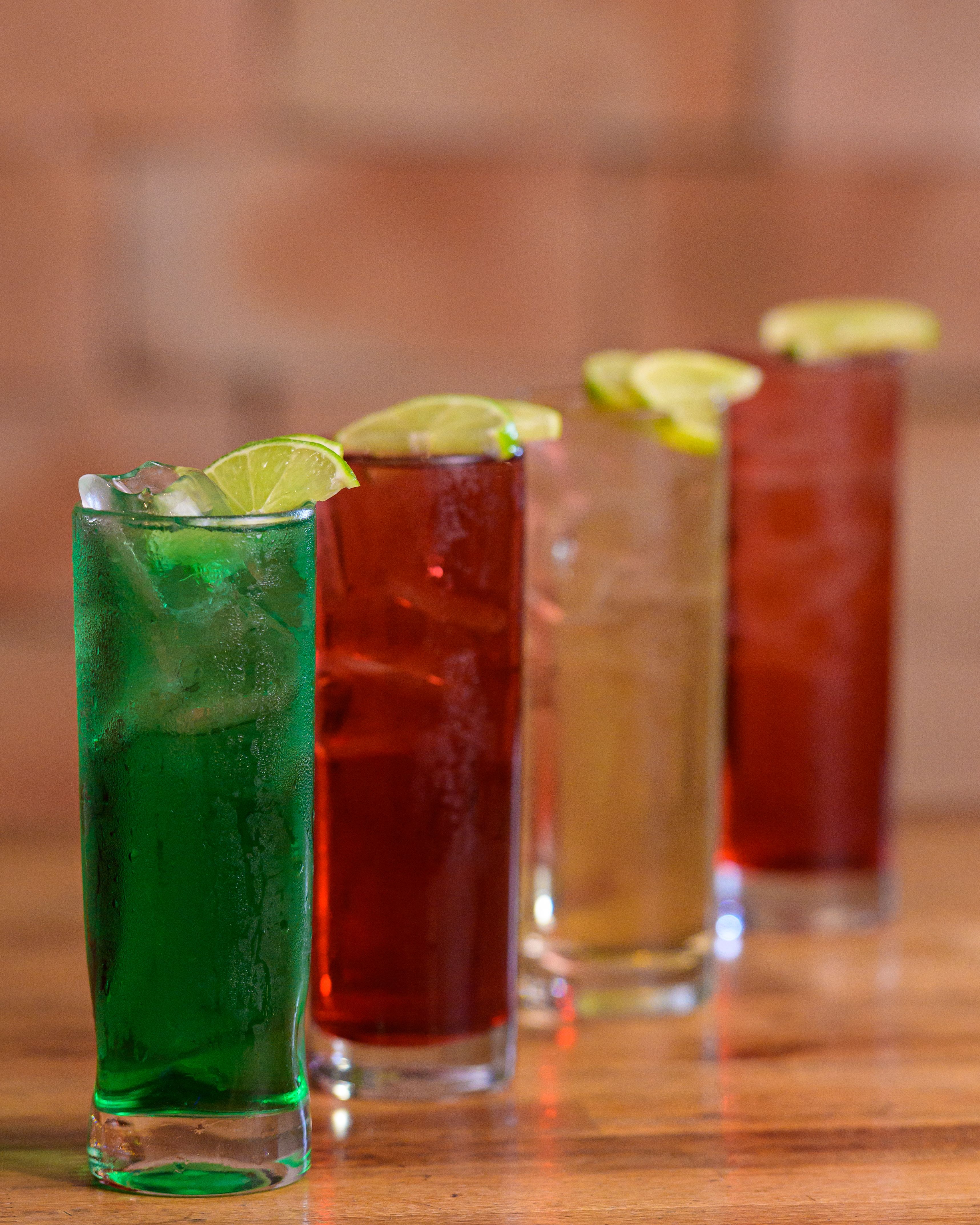 Four High Glasses With Colorful Cocktails Lined Up on a Wooden Table ...