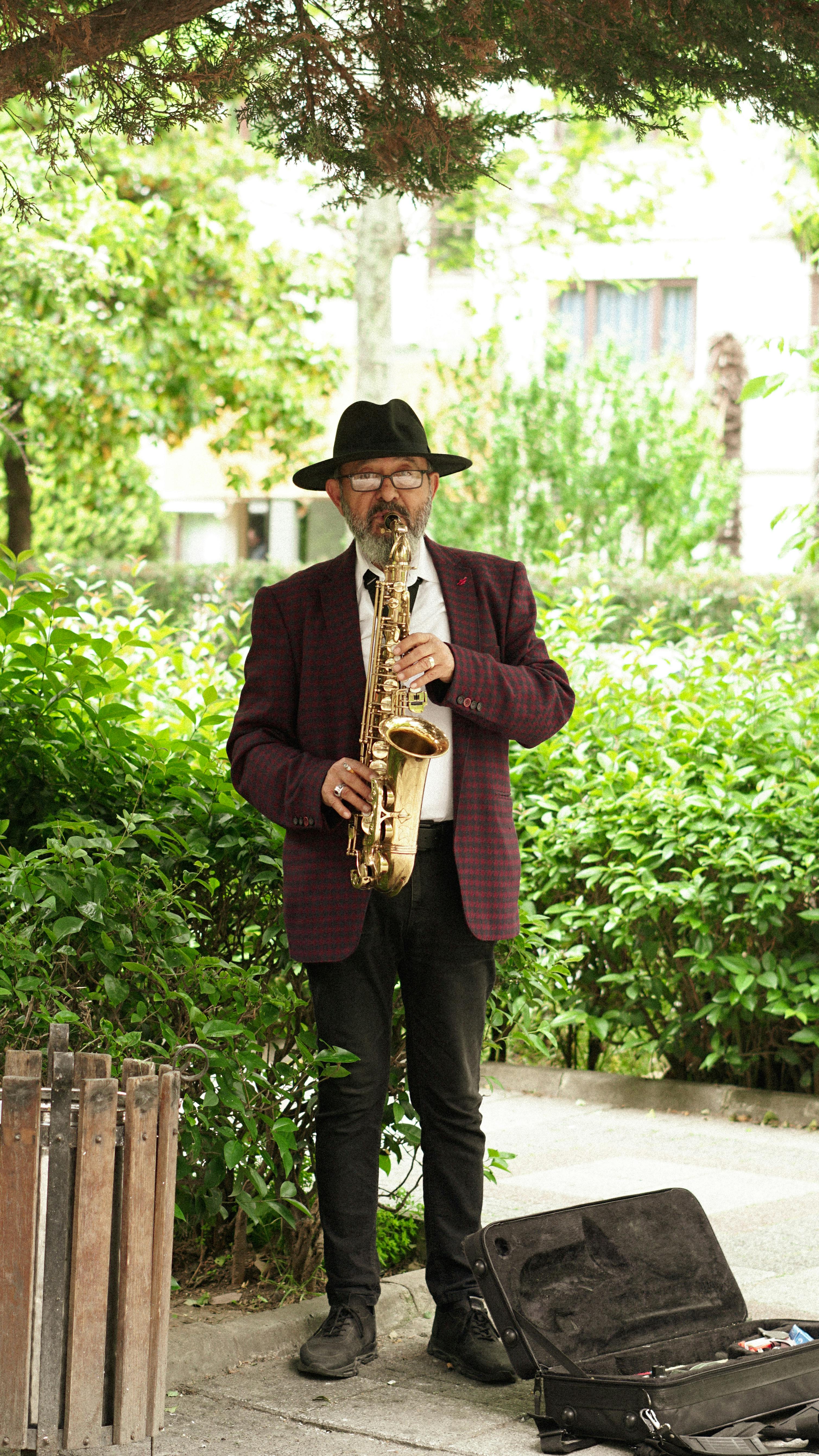 A man in a hat and jacket playing a saxophone · Free Stock Photo