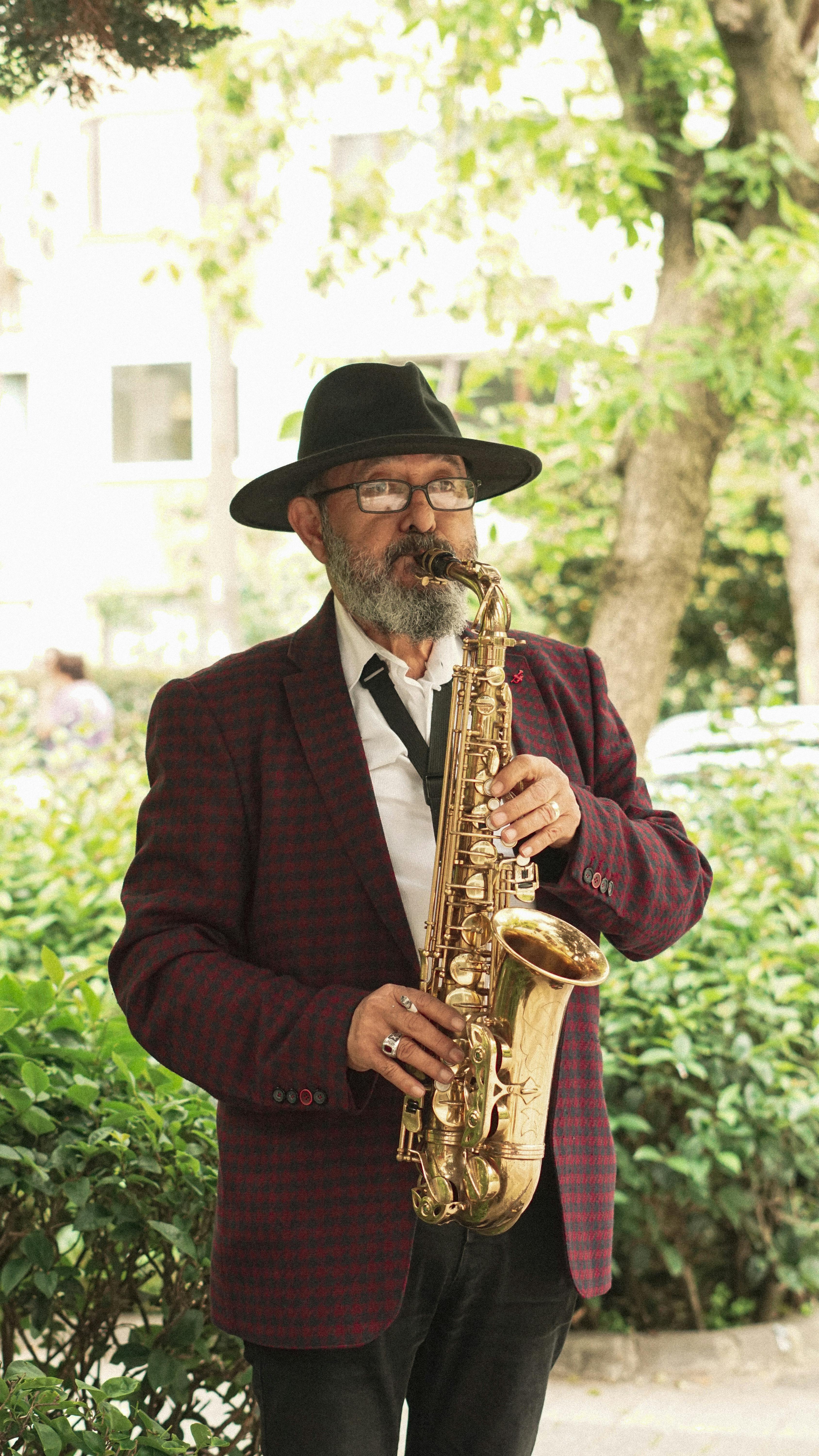 A man in a hat and jacket playing a saxophone · Free Stock Photo