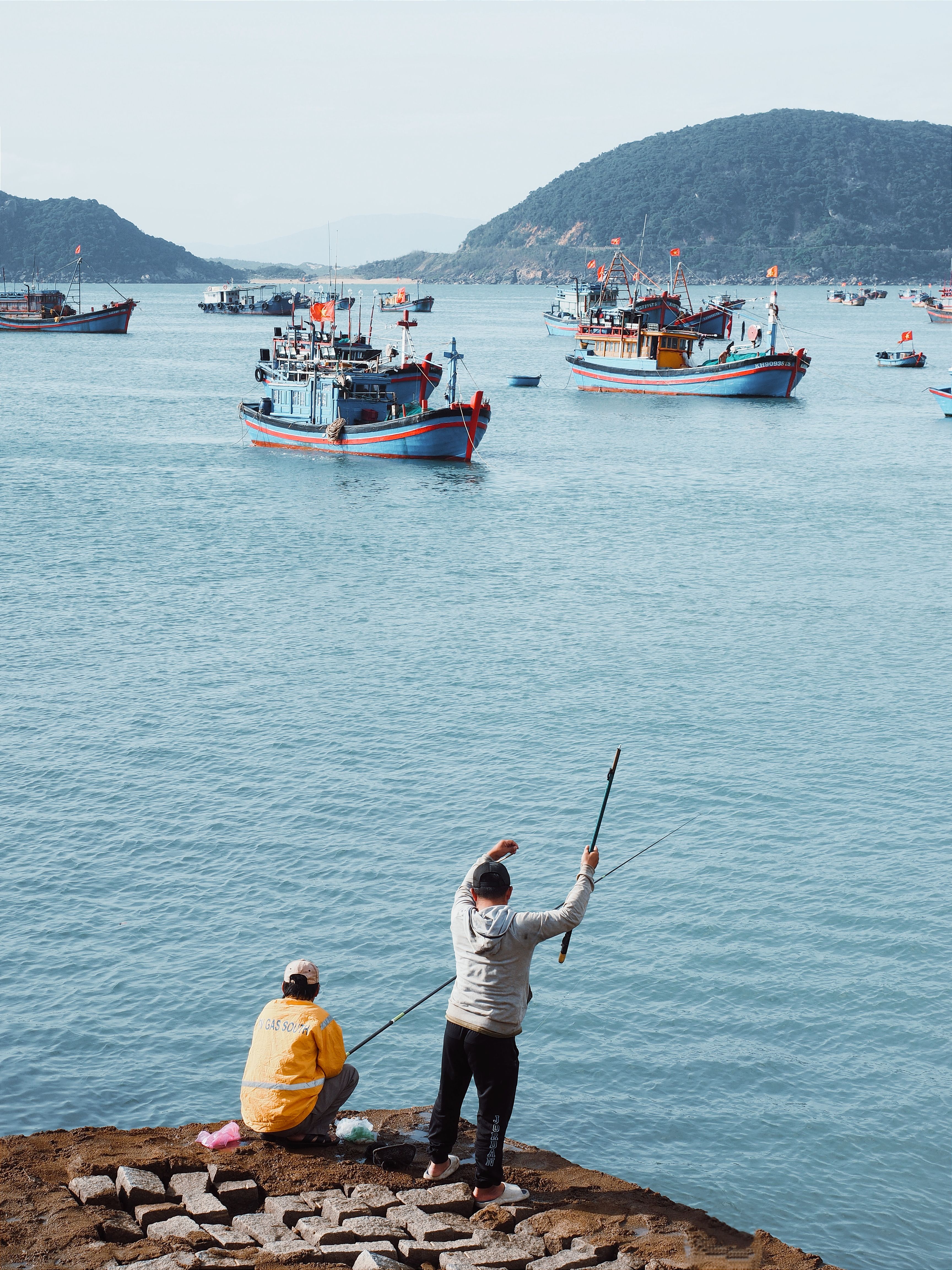 Men Fishing on the Shore and Fishing Boats Sailing in the Bay · Free ...