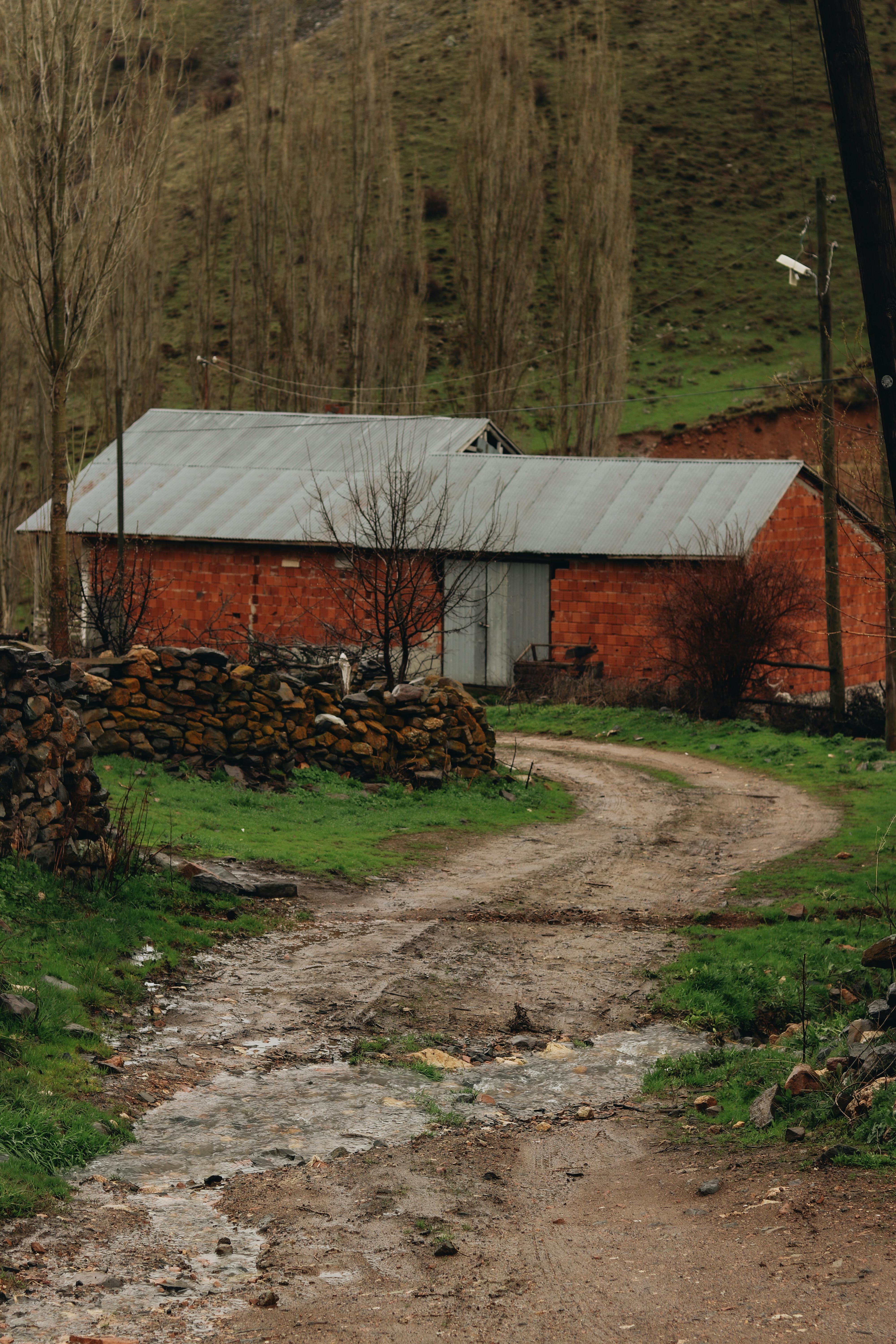 Small Stream Crossing a Muddy Rural Road Leading to Red Brick Shed on a ...