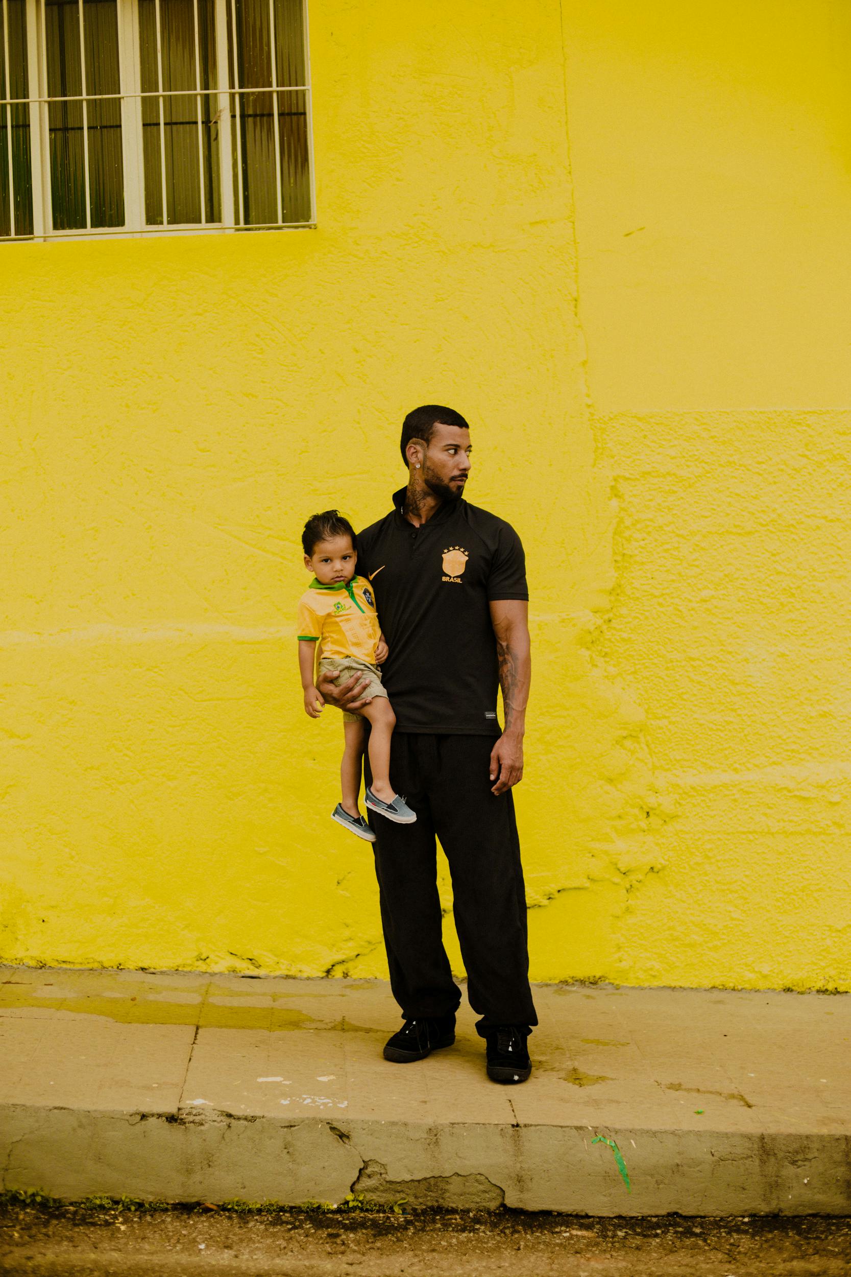 Man Standing on a Sidewalk in front of a Yellow Building and Holding ...