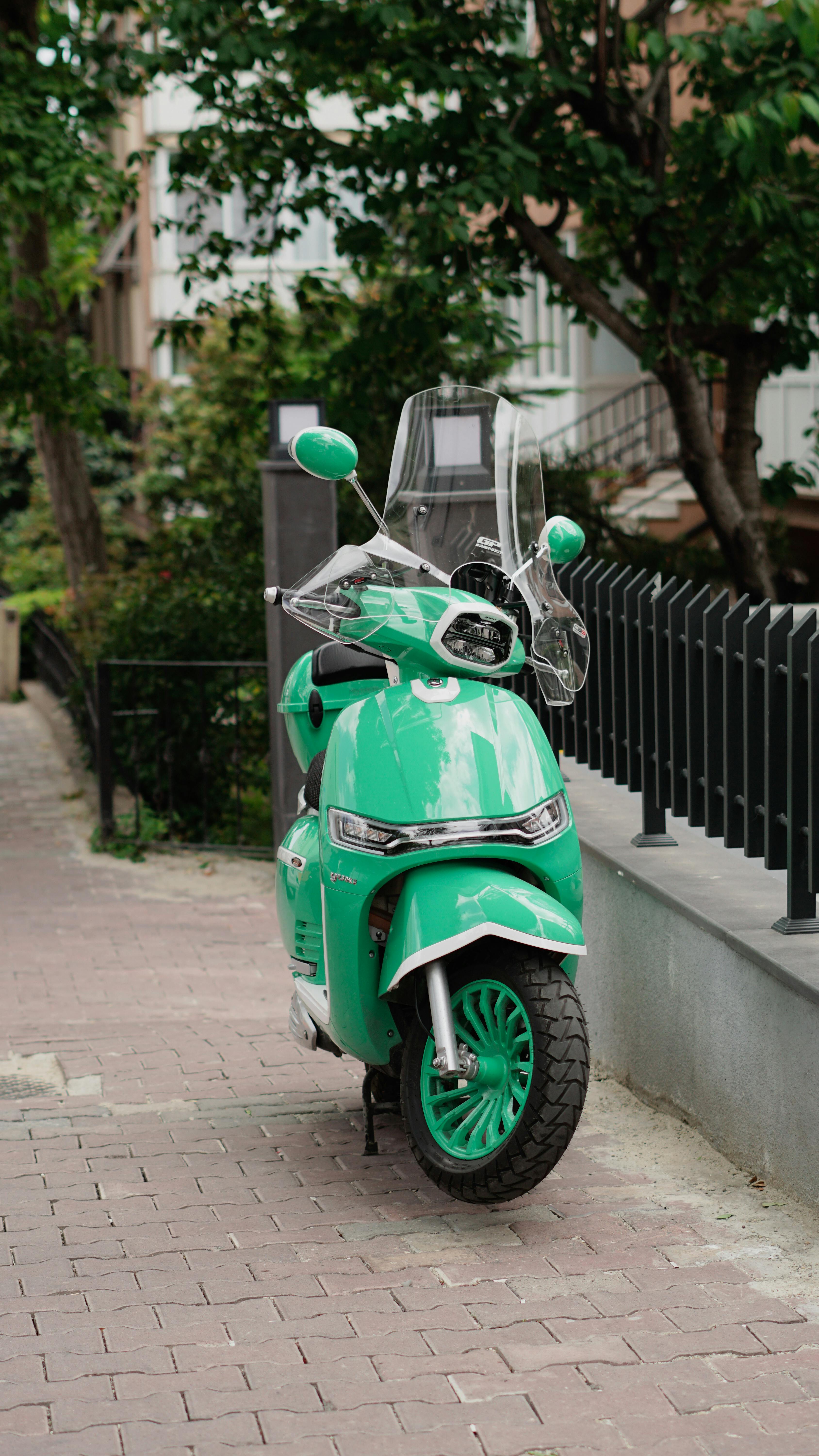 A green moped parked on the sidewalk next to a brick wall · Free Stock ...